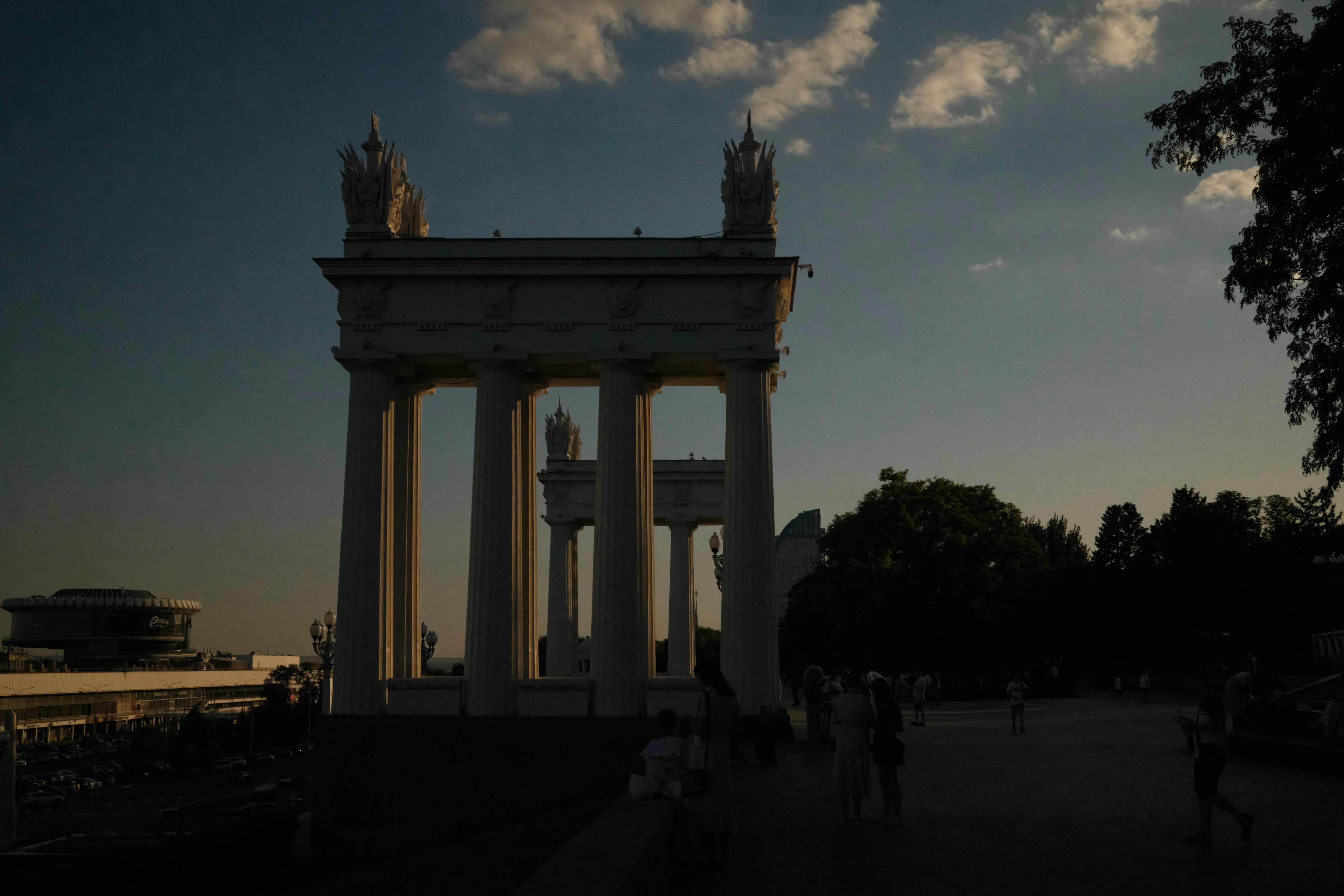 Historic architectural structure framed against a twilight sky, casting long shadows on the ground below.