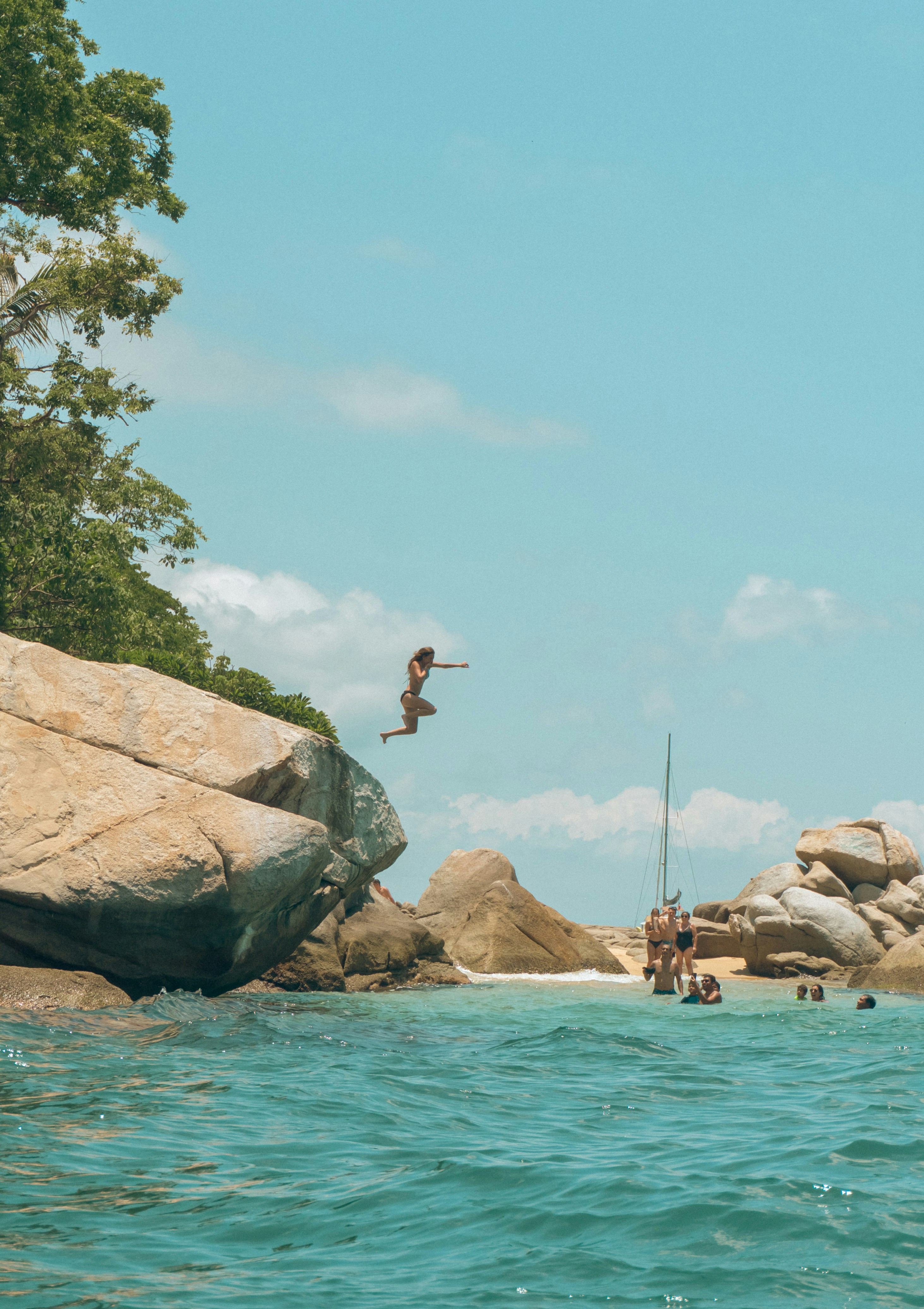 Woman jumps off rocky cliff into blue ocean water