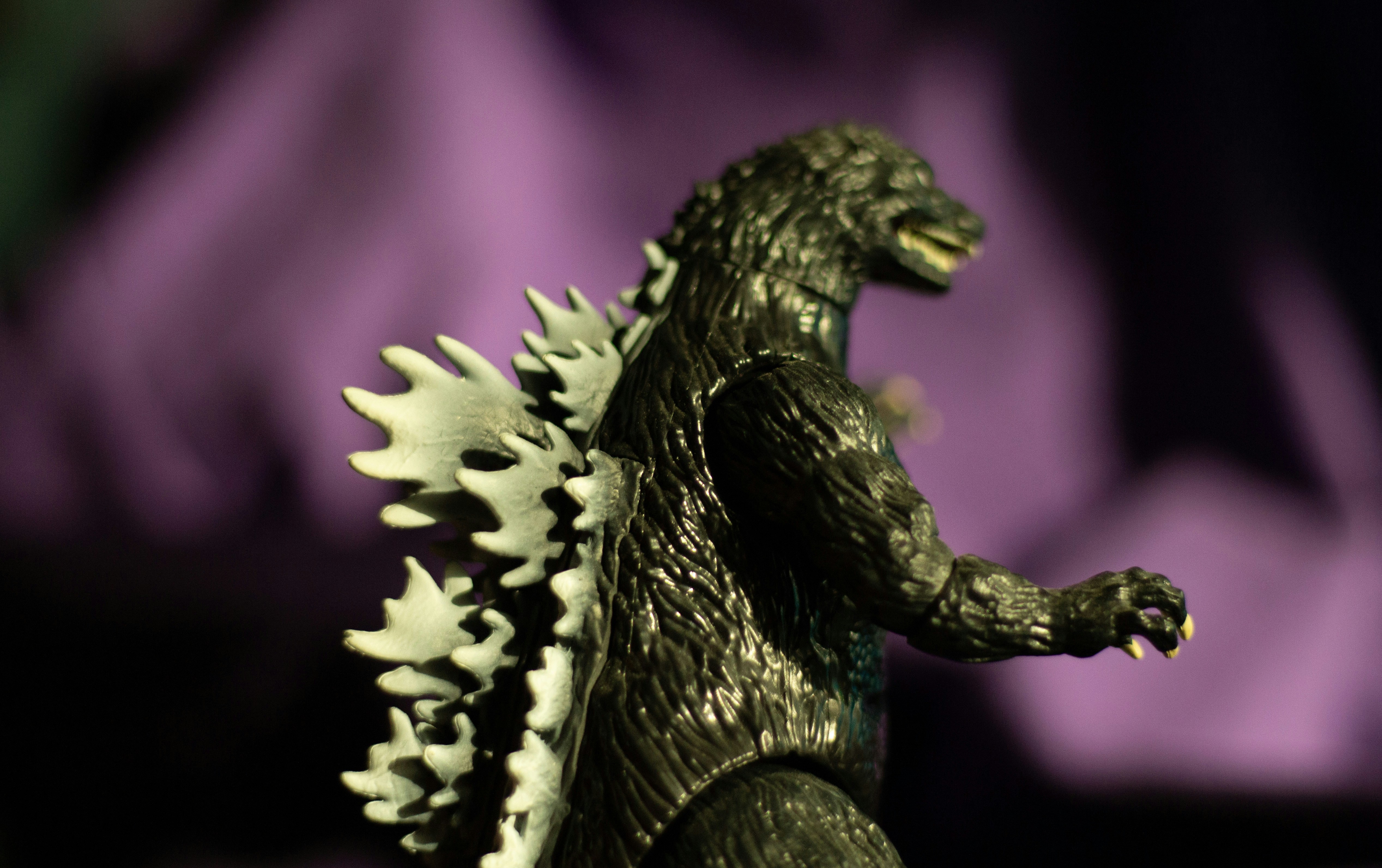 Godzilla figurine poised dramatically against a blurred purple backdrop, showcasing intricate details of its scales and spikes.