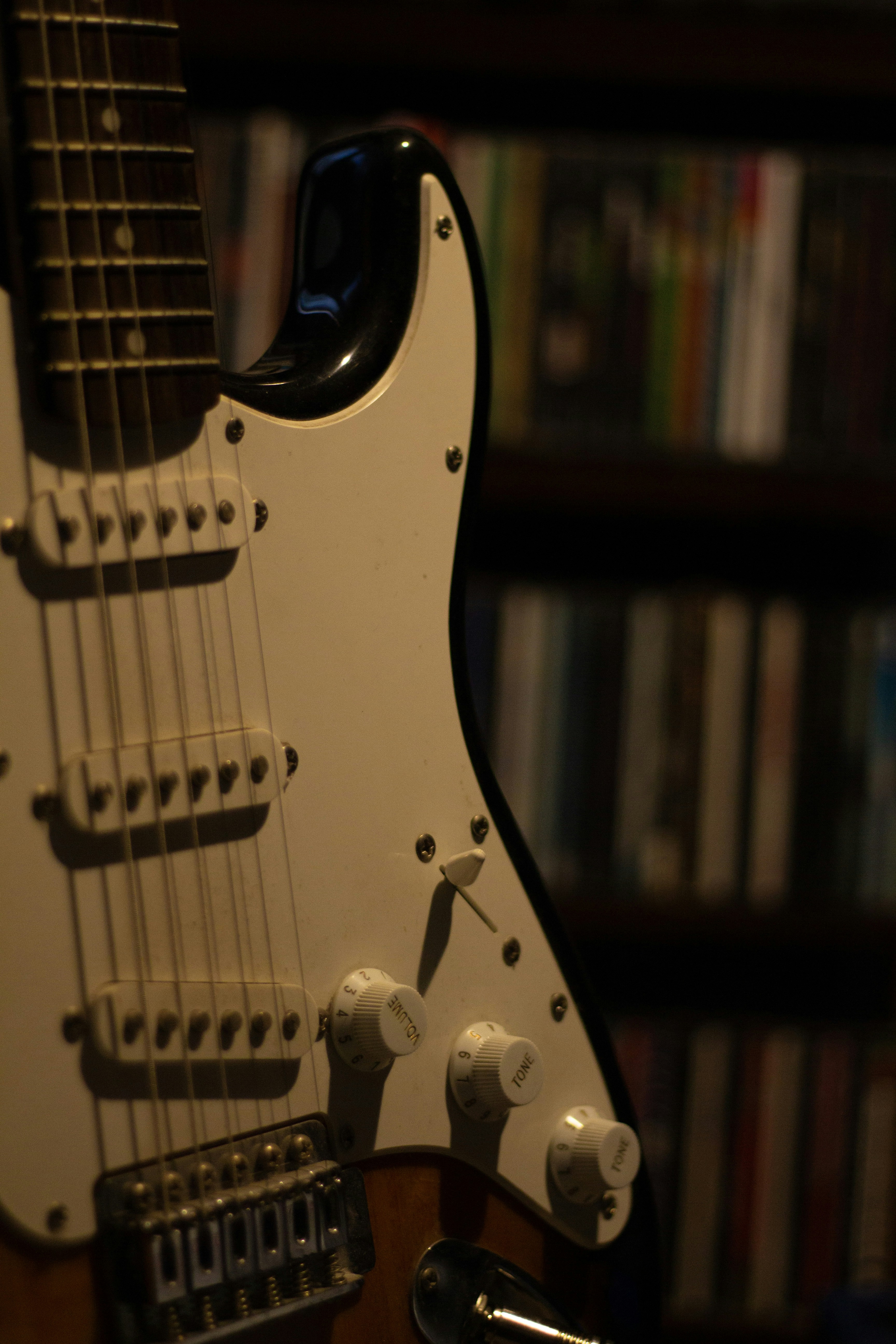 guitar,fender,stratocaster | Close-up of a white electric guitar with bookshelf background bookshelf background books behind it