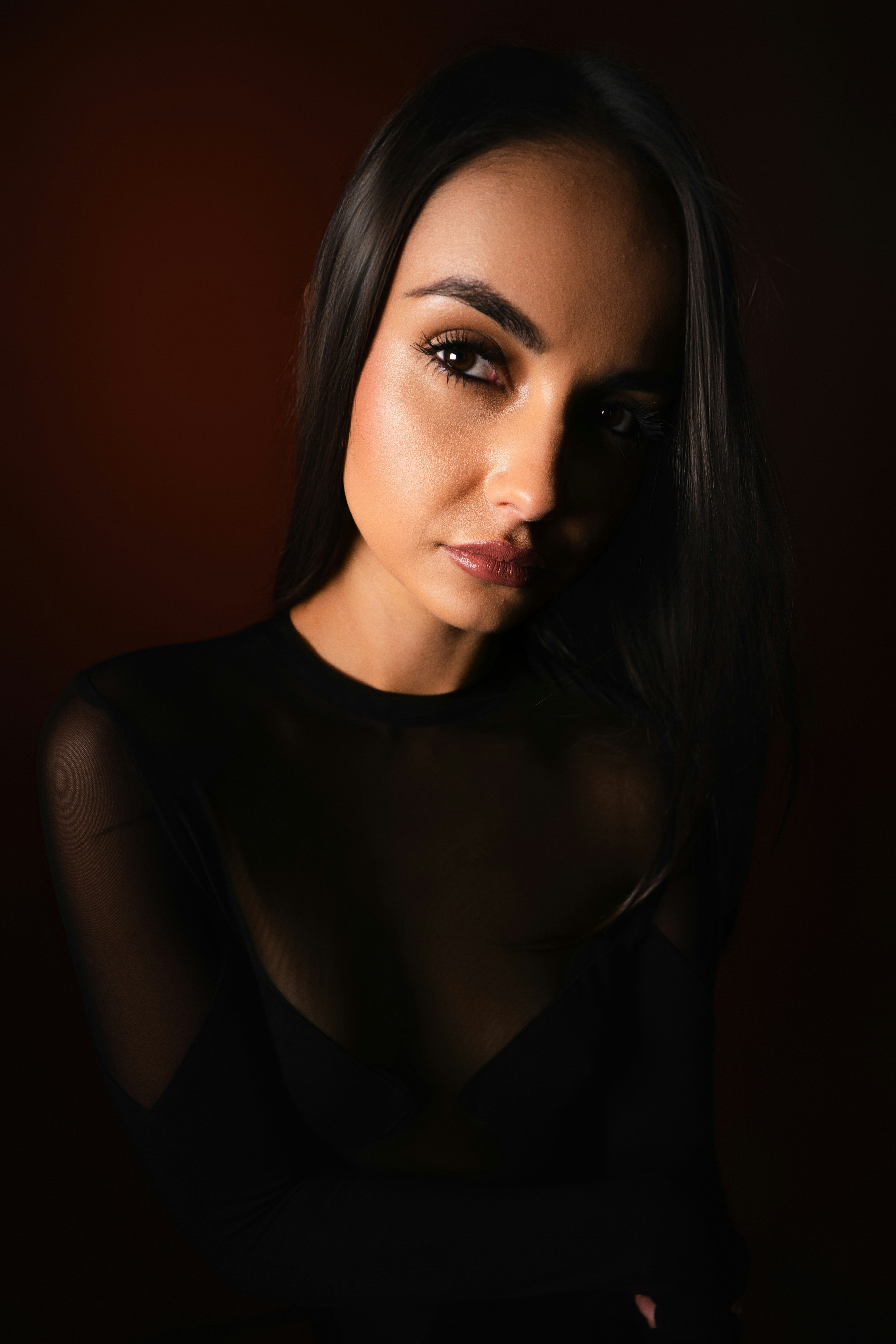 A close-up portrait highlighting a woman's expressive features against a warm, dark background. The interplay of light accentuates her serene gaze.