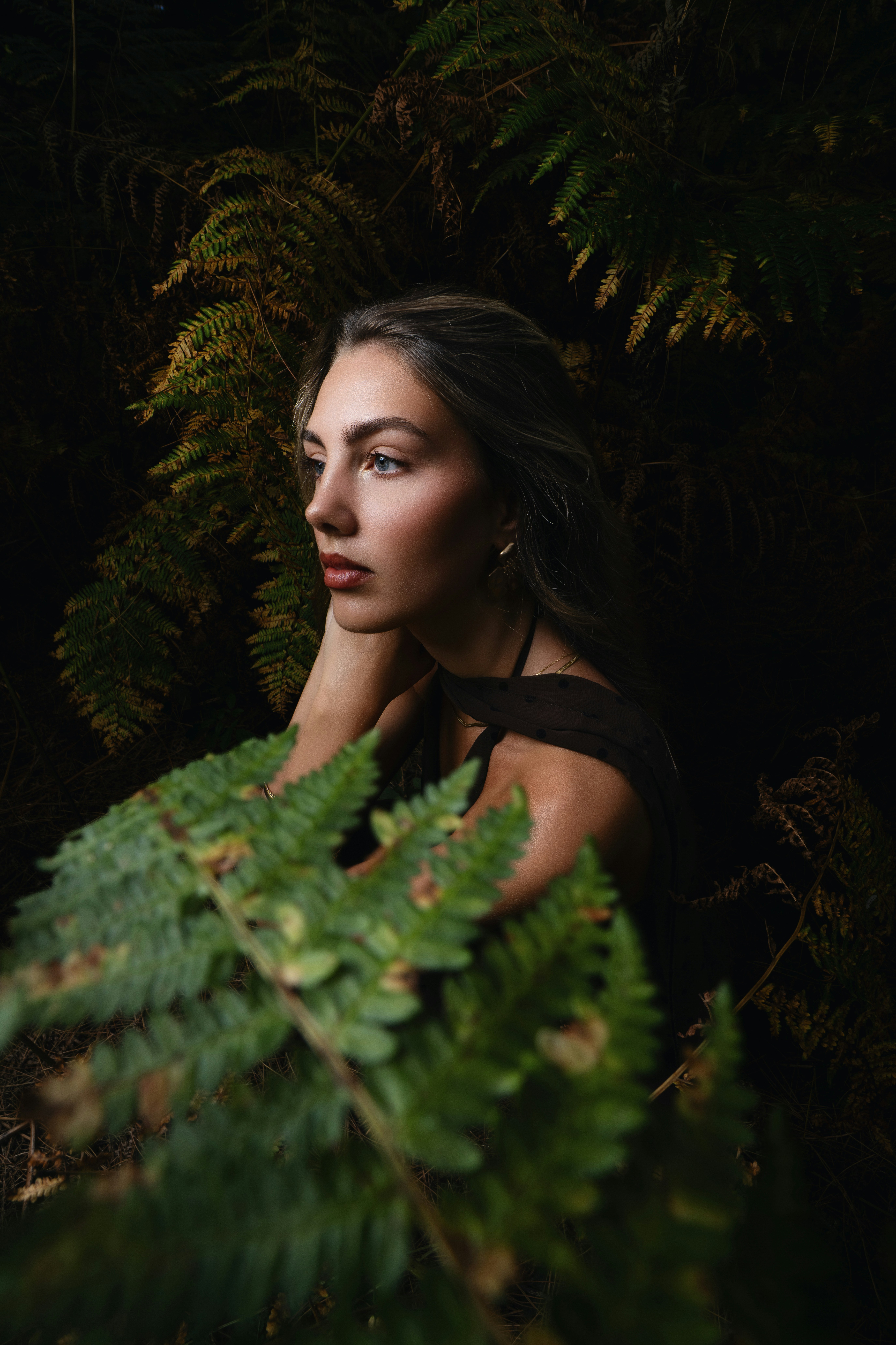 Woman posing among lush green ferns and foliage.
