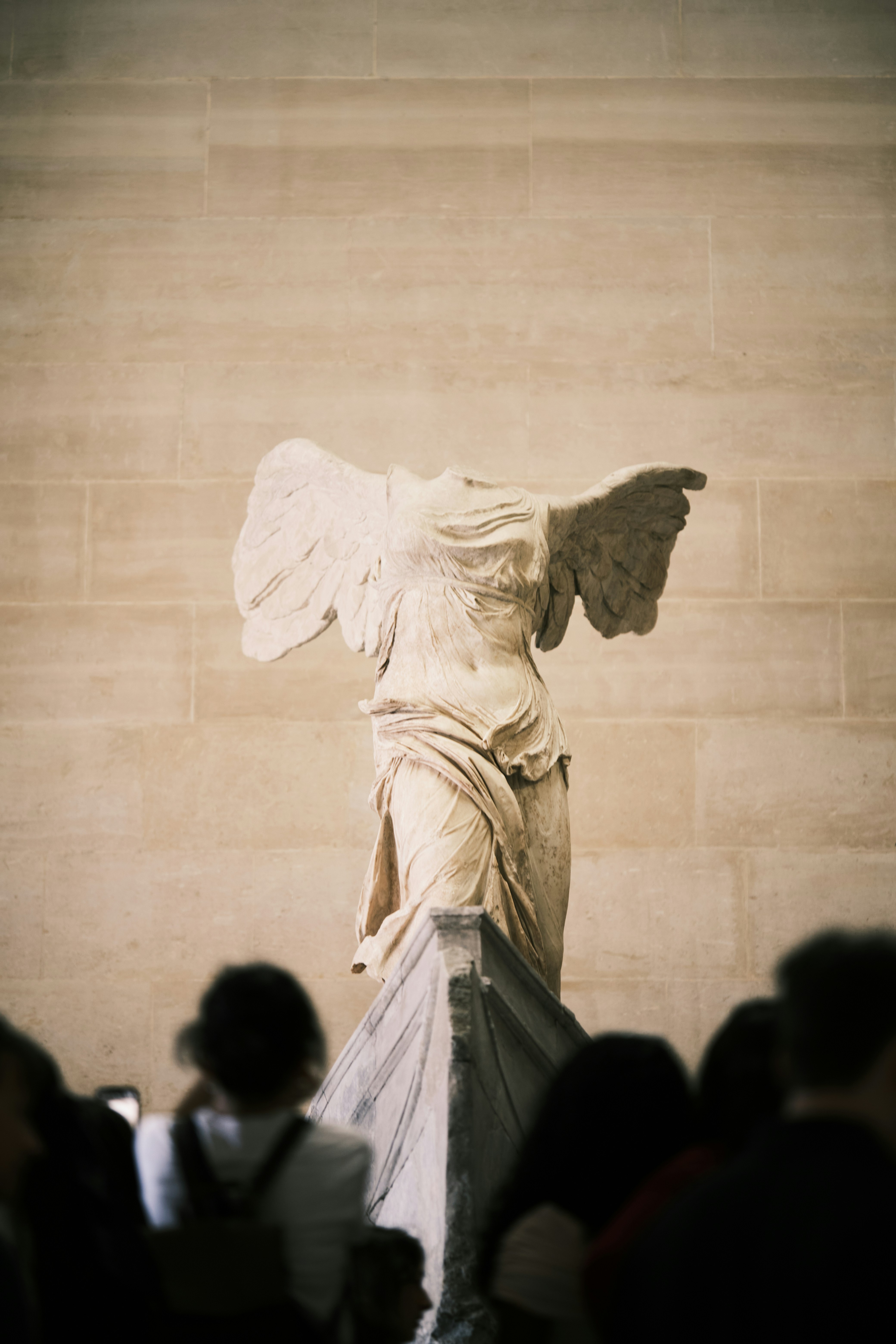 Winged Victory of Samothrace stands majestically on its pedestal, embodying triumph and grace amidst a crowd of admirers.