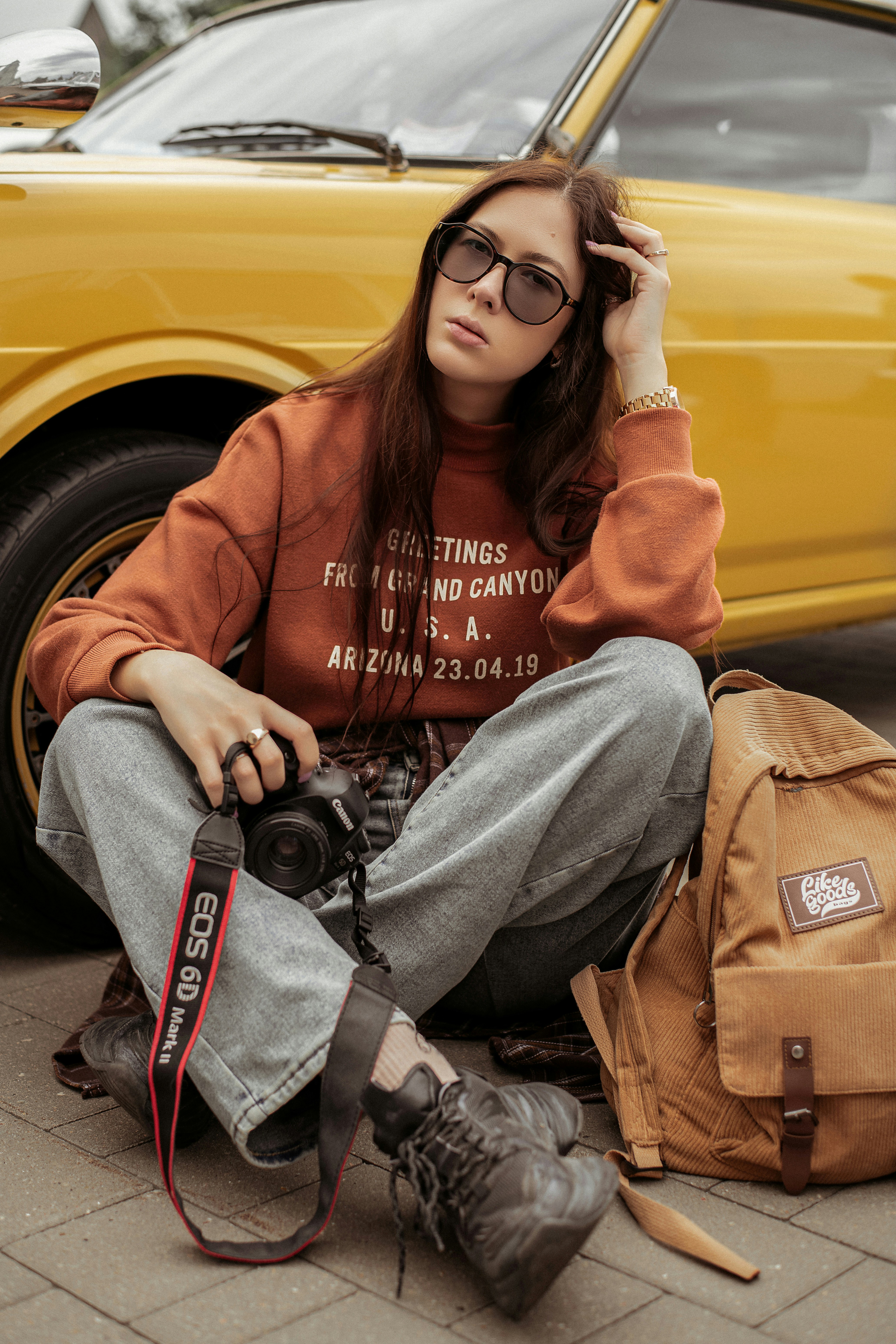 Girl with camera and car | Woman with camera sits by yellow car with backpack