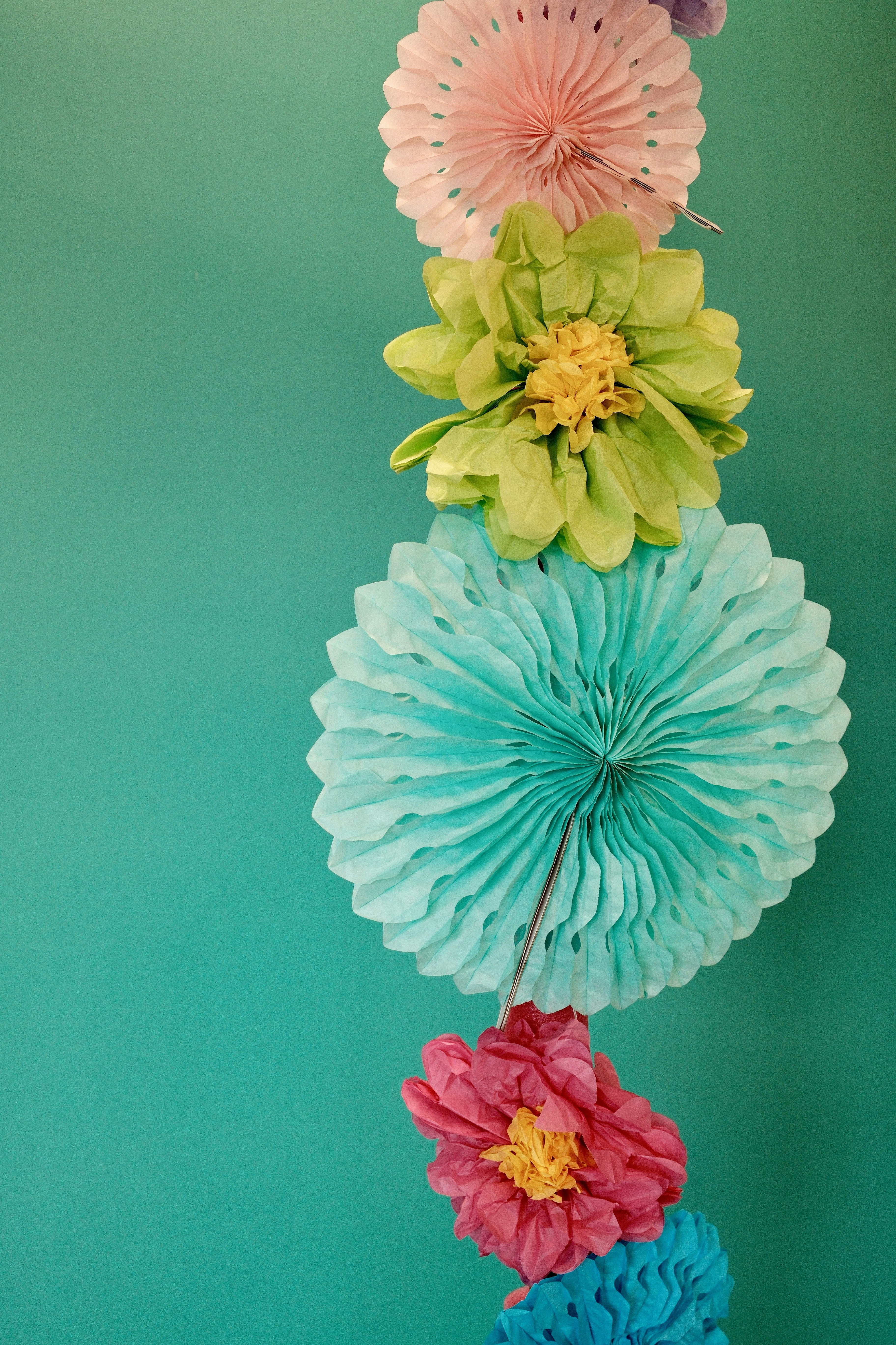 Colorful paper flowers hanging against a vibrant teal backdrop, creating a playful and festive atmosphere.