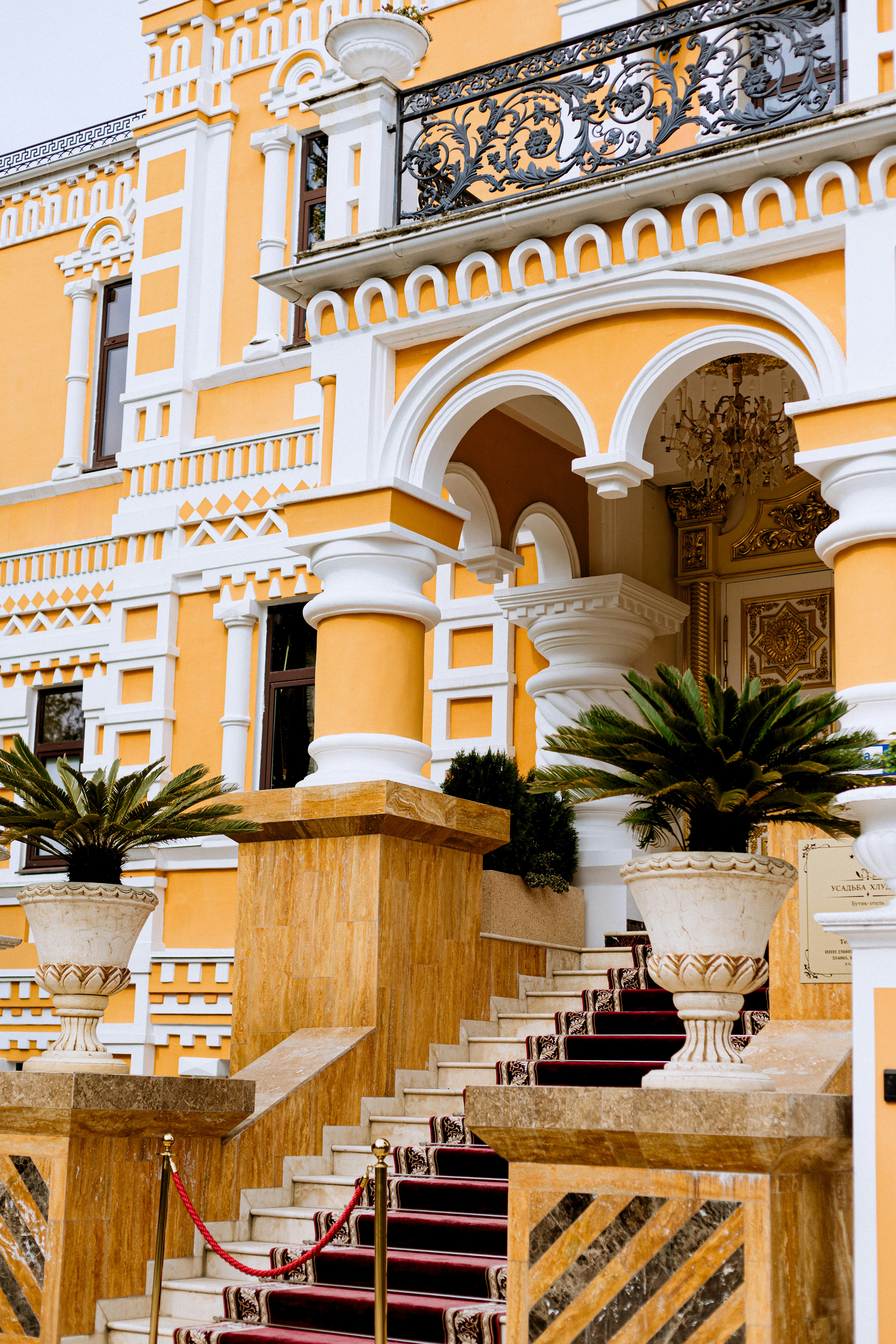 Ornate staircase leading to a grand entrance adorned with vibrant yellow walls and lush greenery in decorative pots.