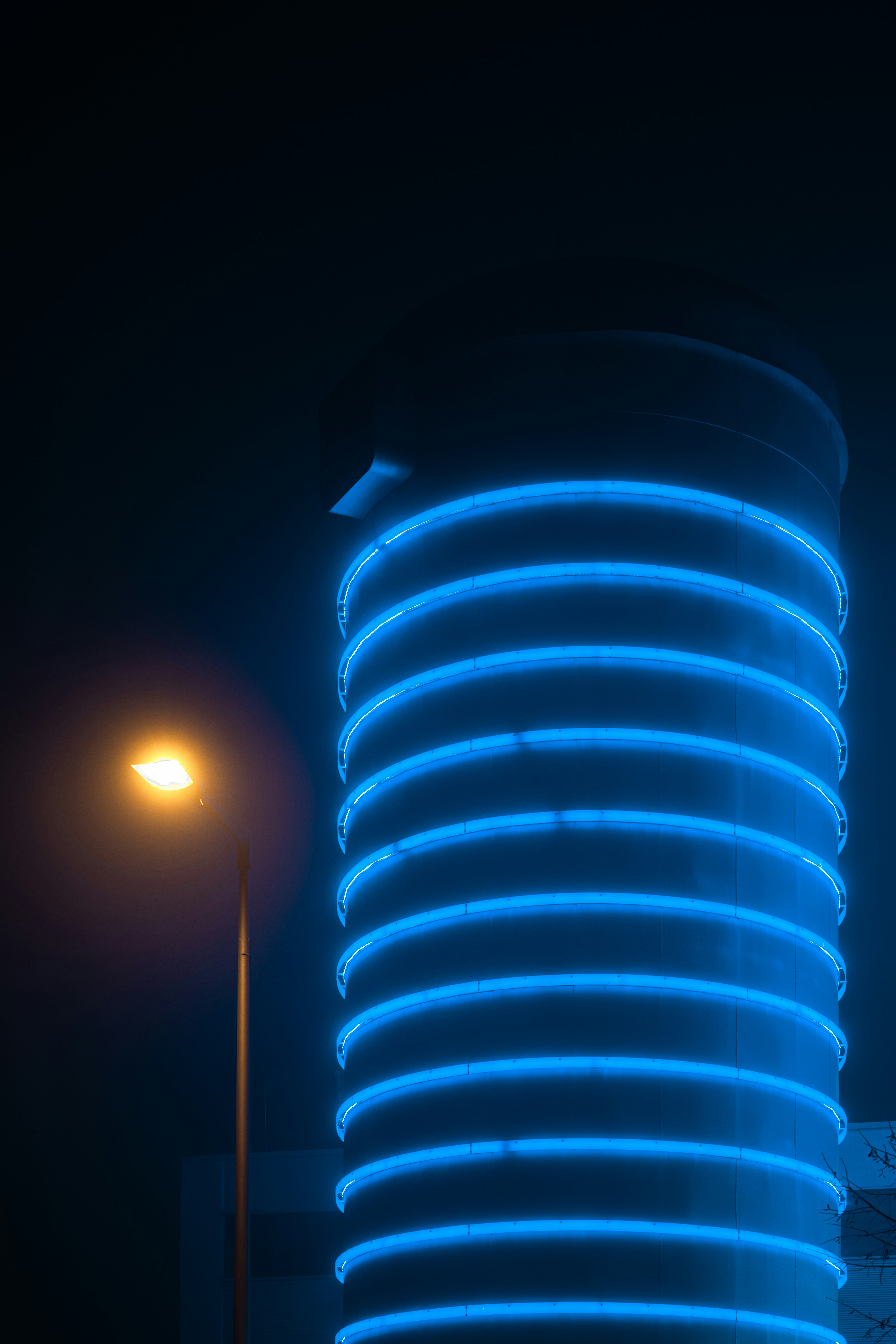 Blue Neon Cylinder: A Night Coil Tower Illuminates the Street