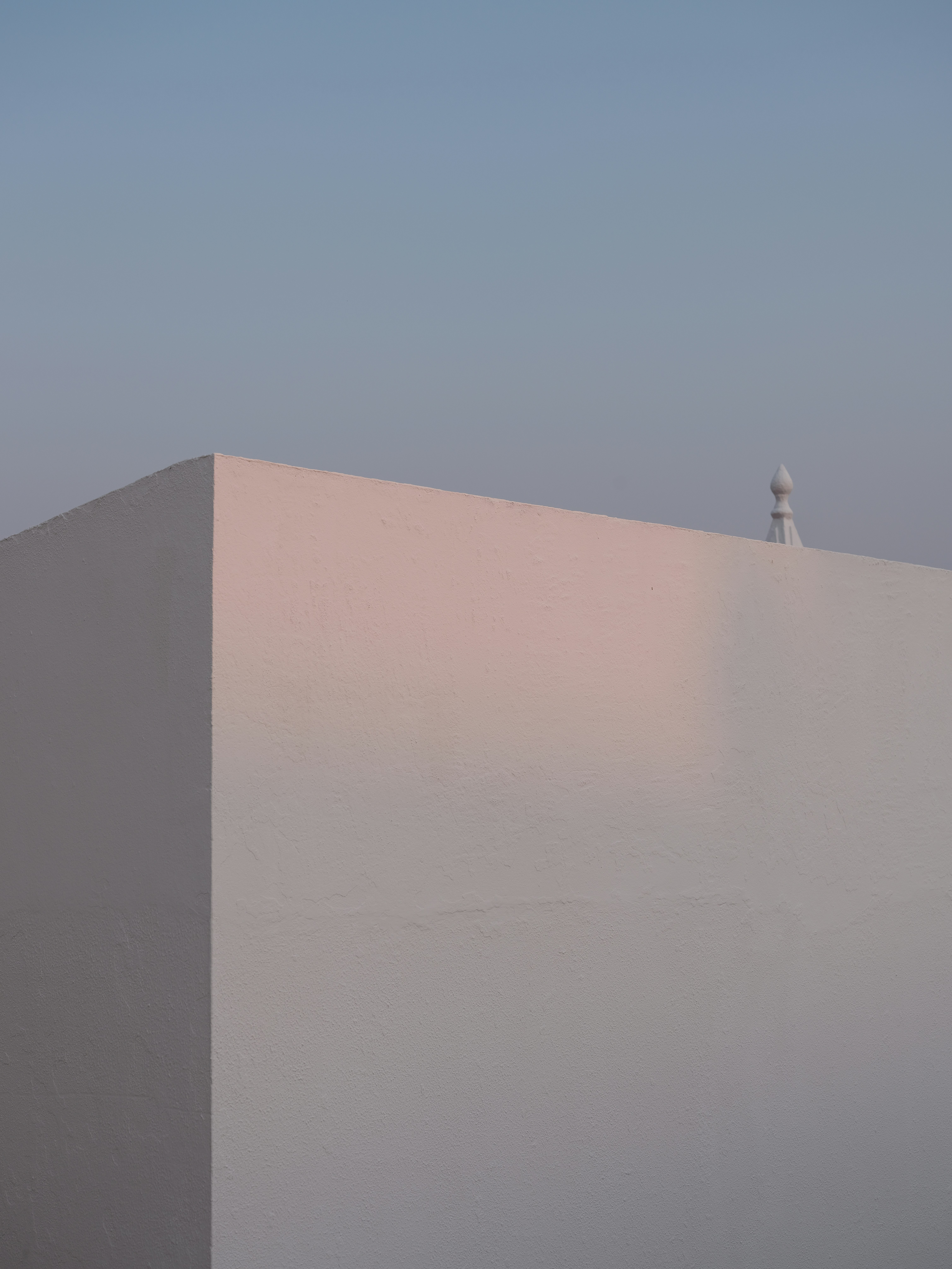 I could return here endlessly, and each time something would remain. The ordinary resists, and then yields, becoming a vessel for memory. | Minimalist white building corner against soft sky