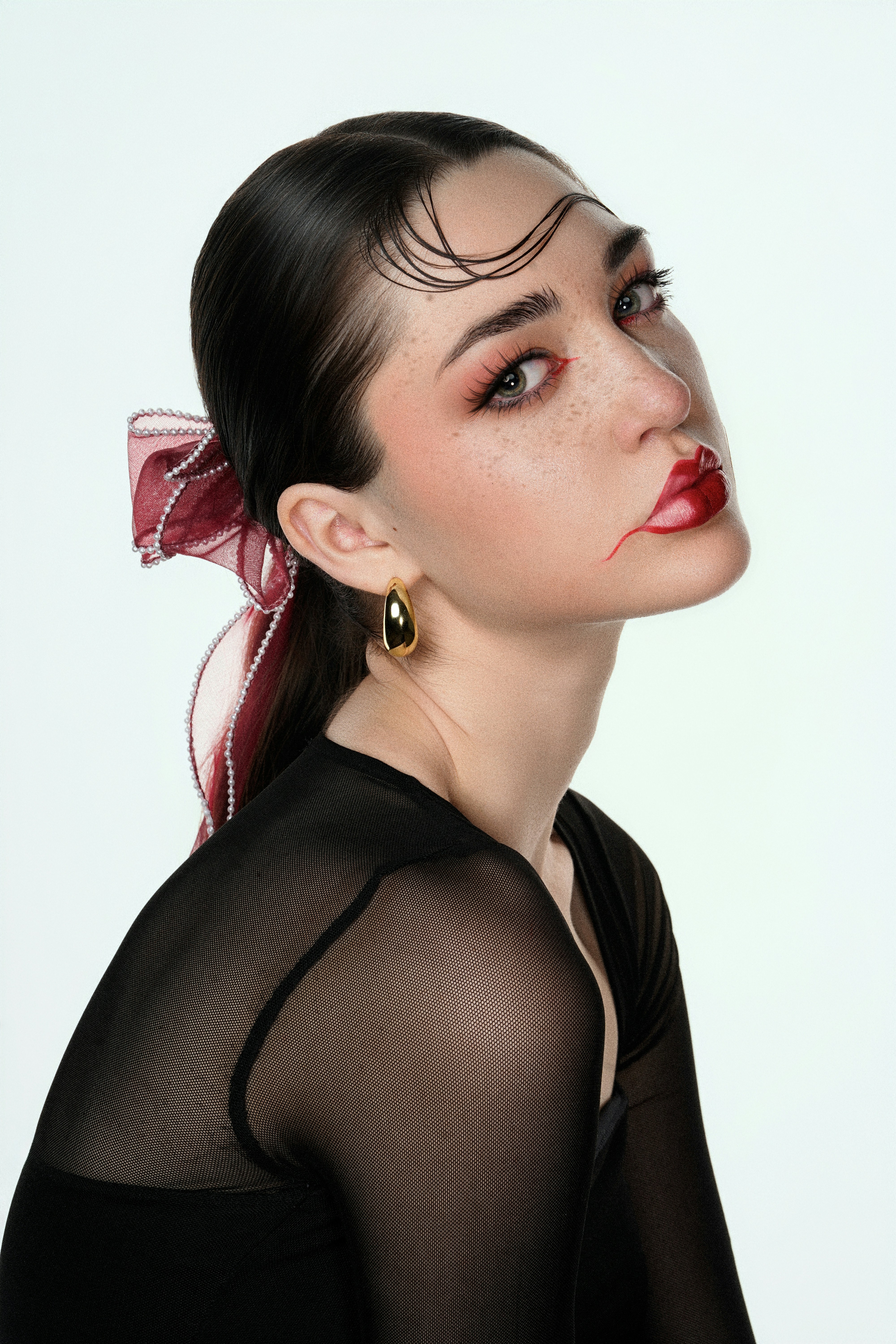 A model with striking makeup featuring red accents and a delicate ribbon in her hair, exuding a blend of elegance and artistry.