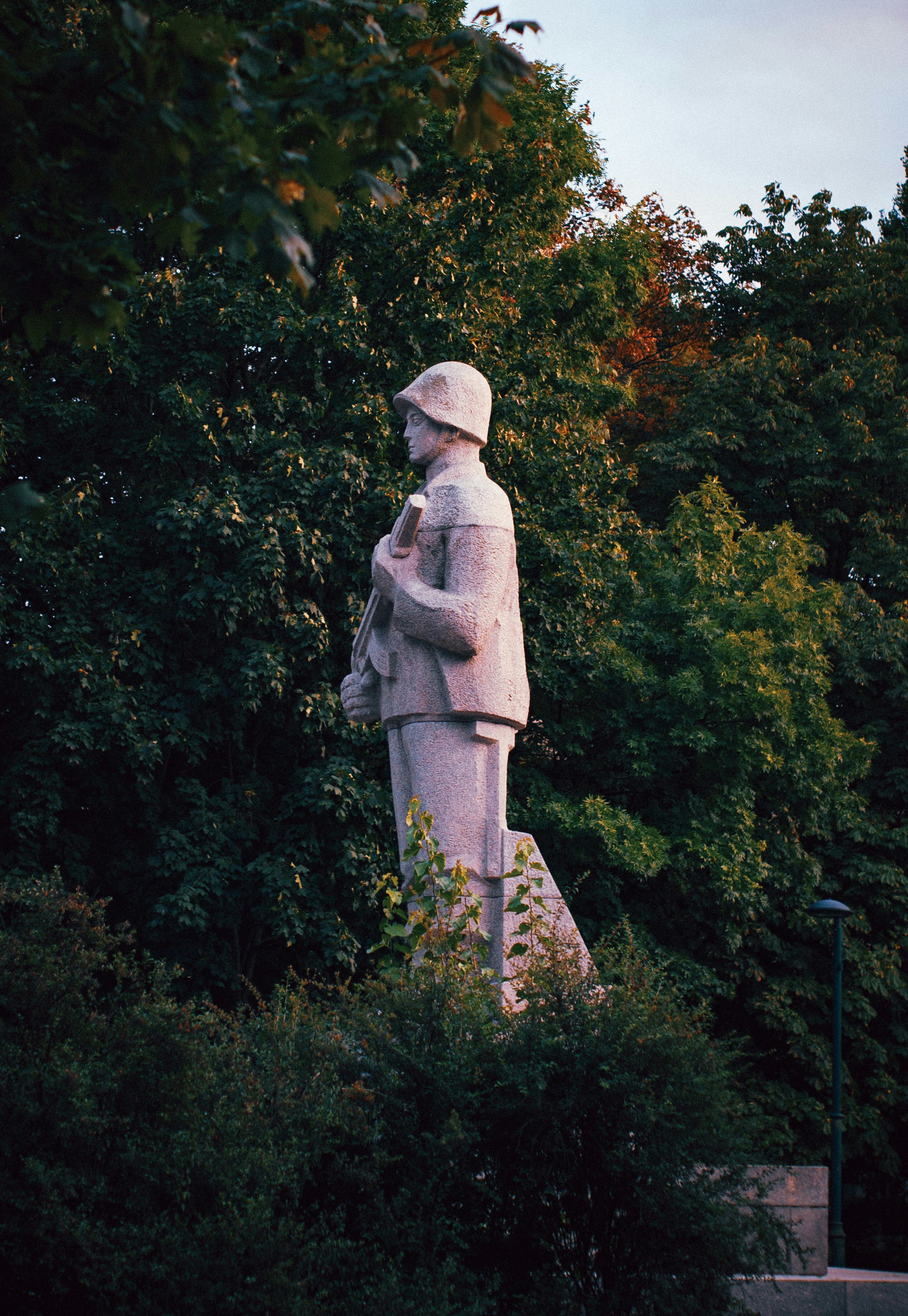 Granite statue of a soldier standing amidst lush greenery, symbolizing remembrance and honor.