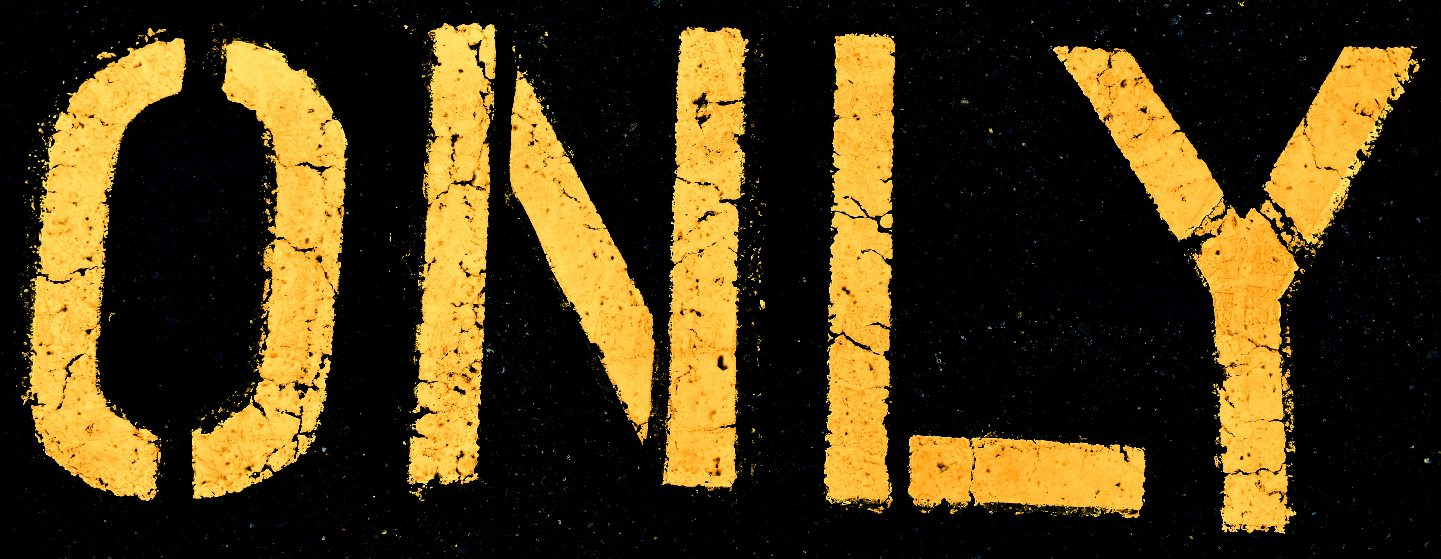 The word ‘only’ painted in bold yellow letters on a street | Yellow word only on black background