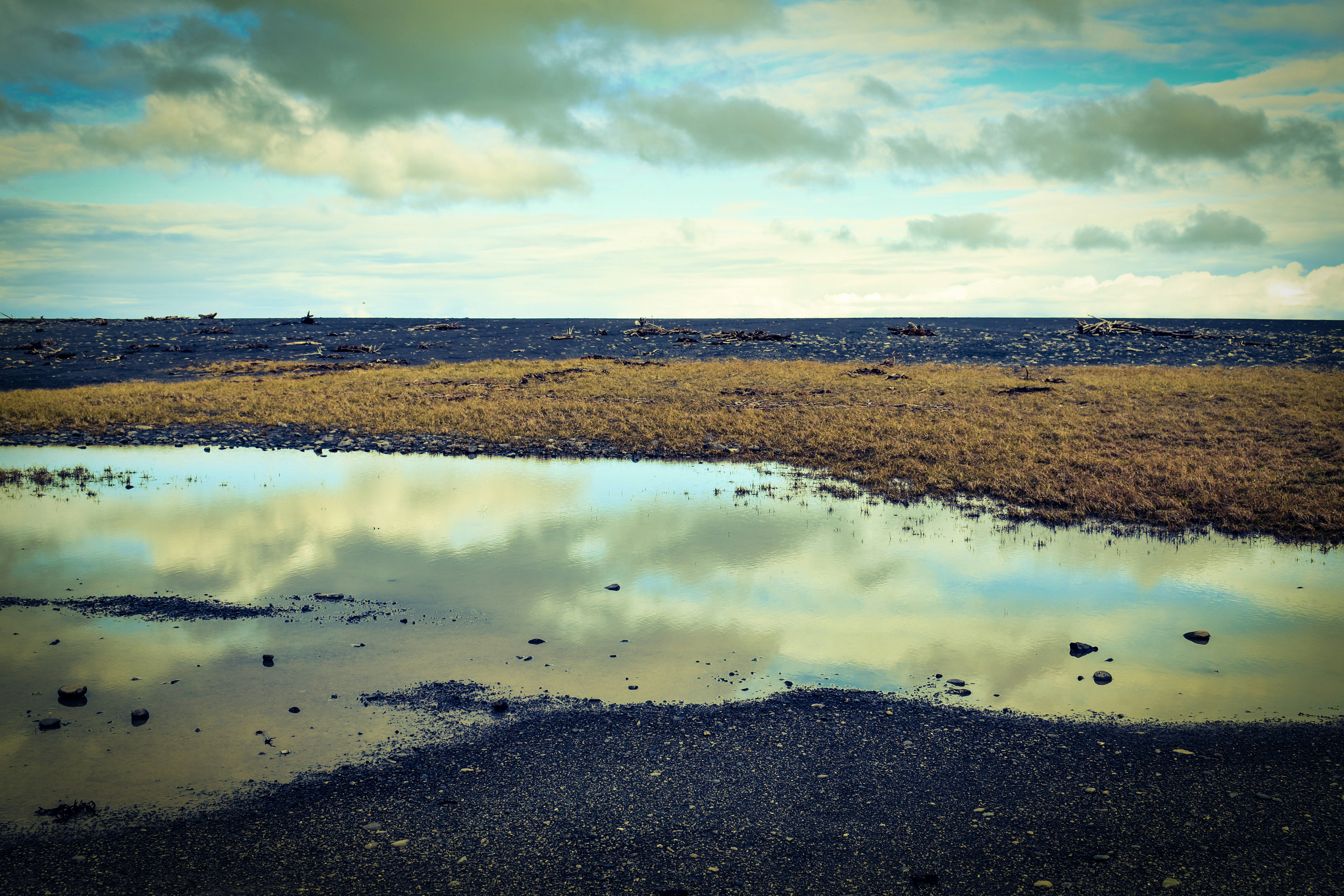A pebble beach with a large water puddle | Clouds reflected in a shallow body of water