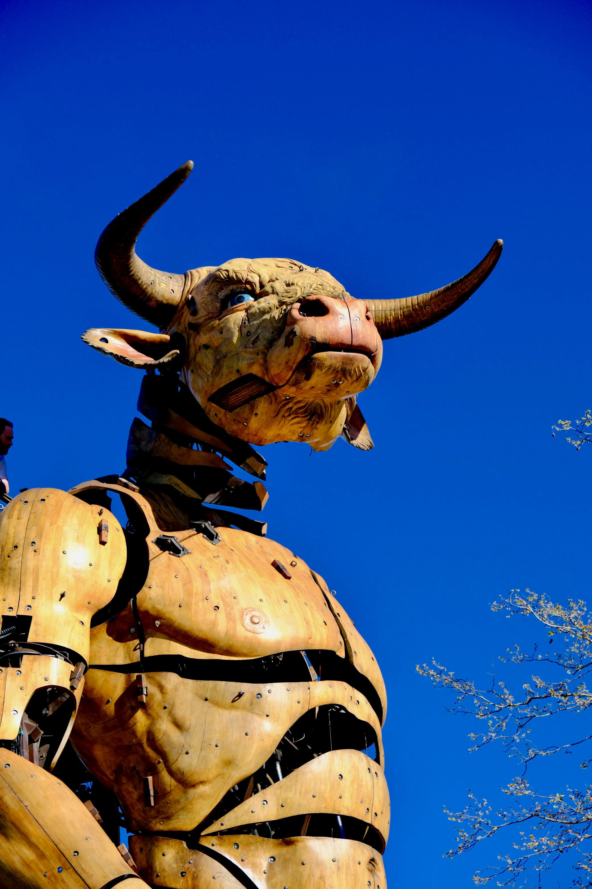 The minotaur who walks around the town at Halle de La Machine, Tolouse, France. | Giant wooden bull-man sculpture against blue sky