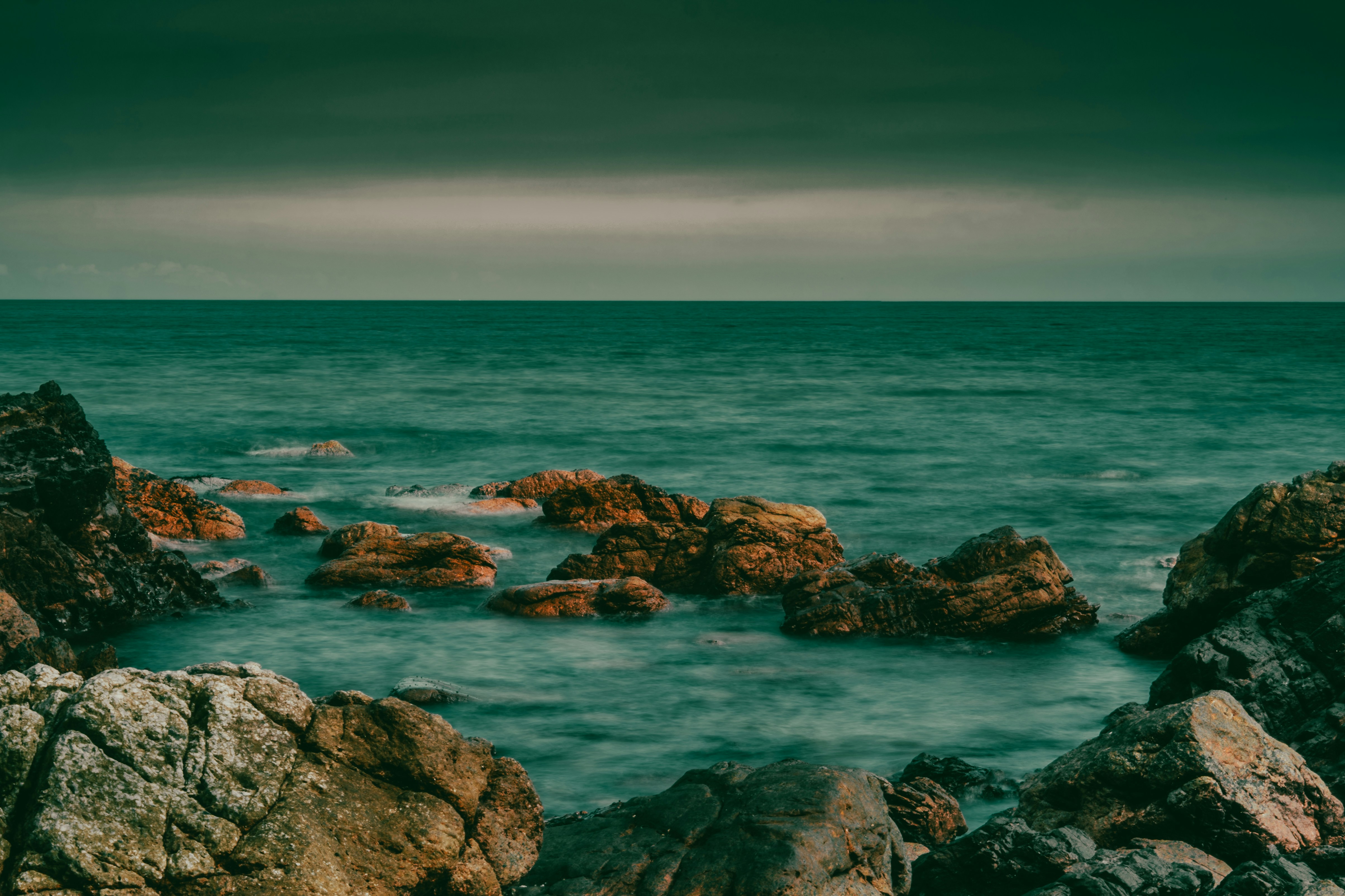 seaside stones | Rocky coastline with calm ocean waves under stormy sky