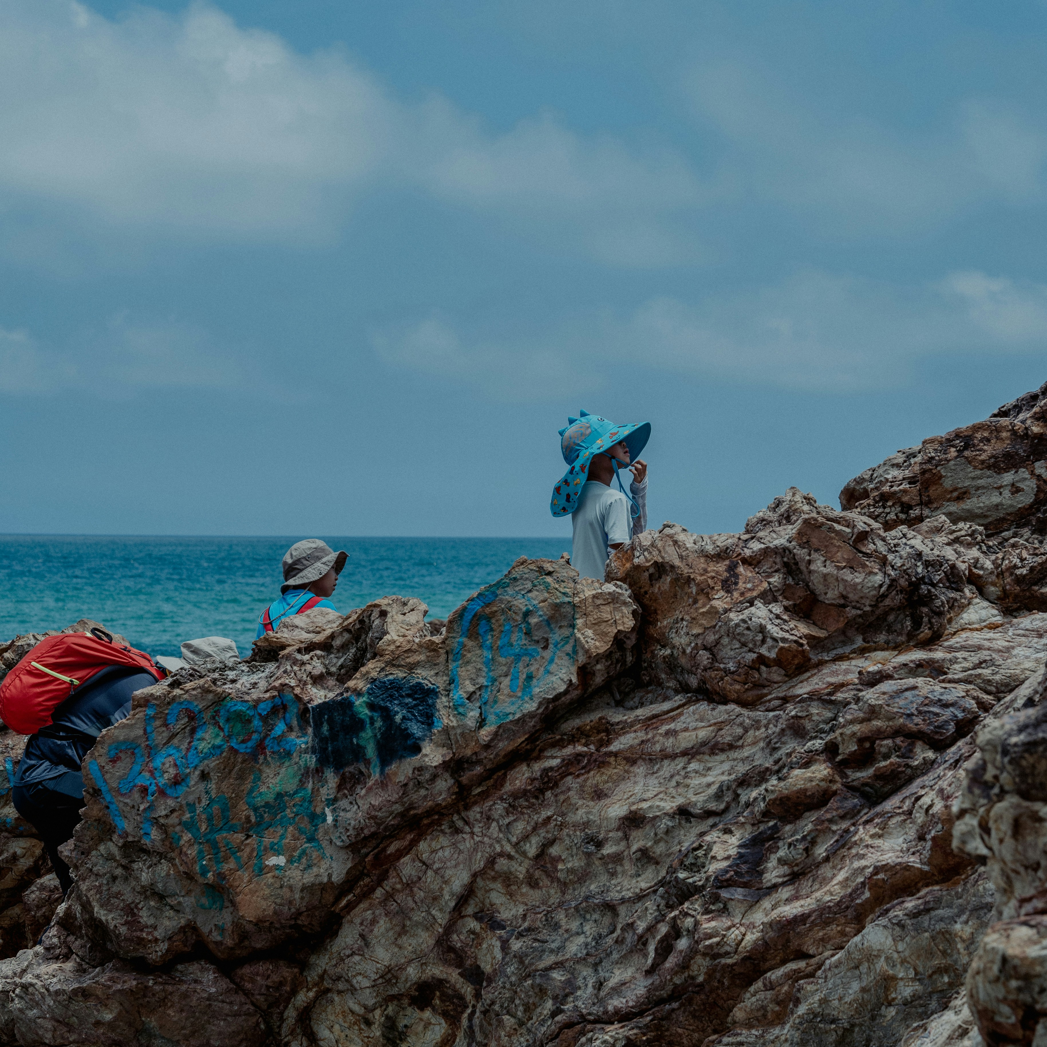 Blue-Hatted Figure at the Edge of the Sea-Rock Ridge