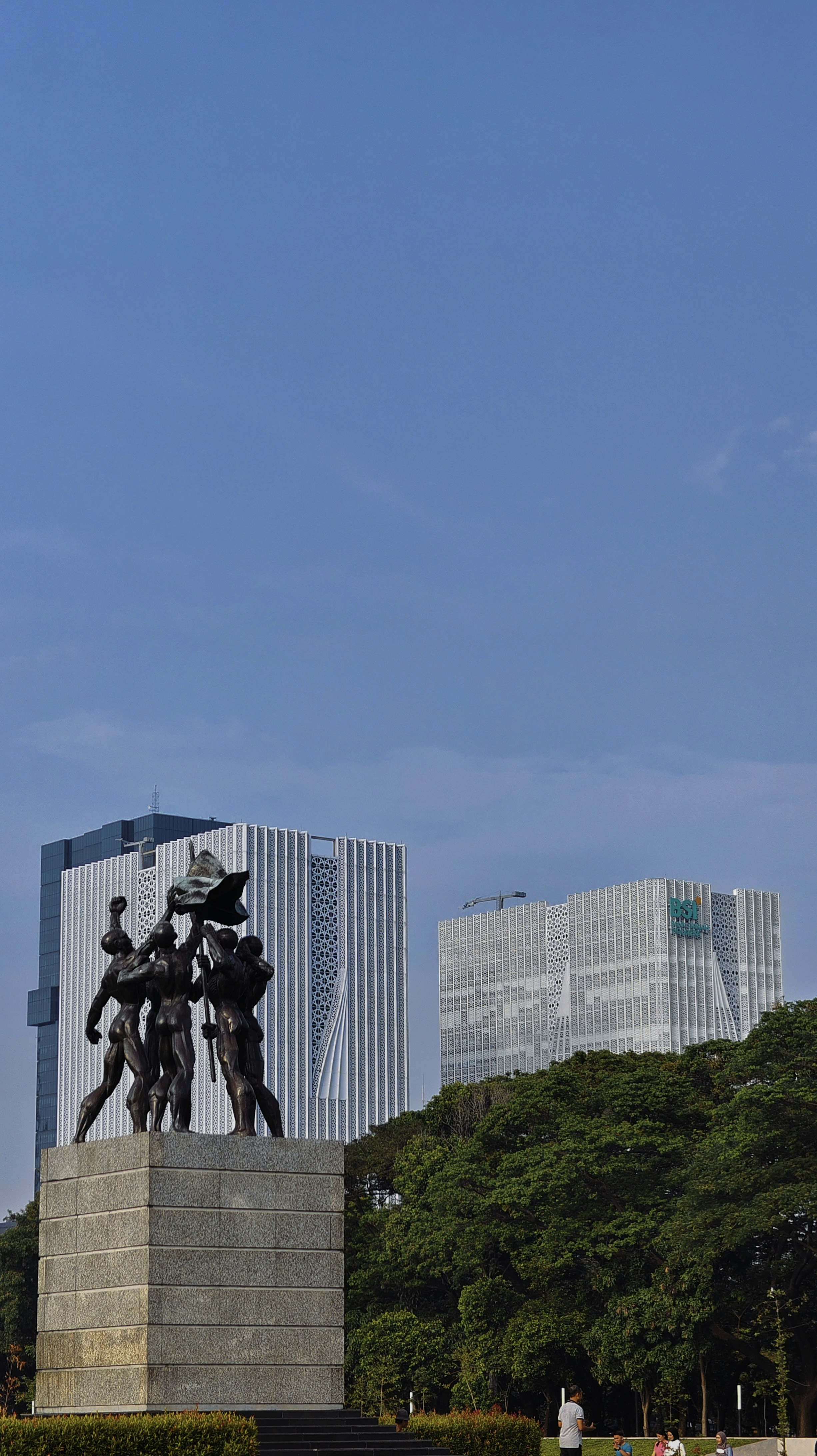 Bronze sculpture depicting a group of figures in dynamic poses, set against a backdrop of modern architecture and greenery.