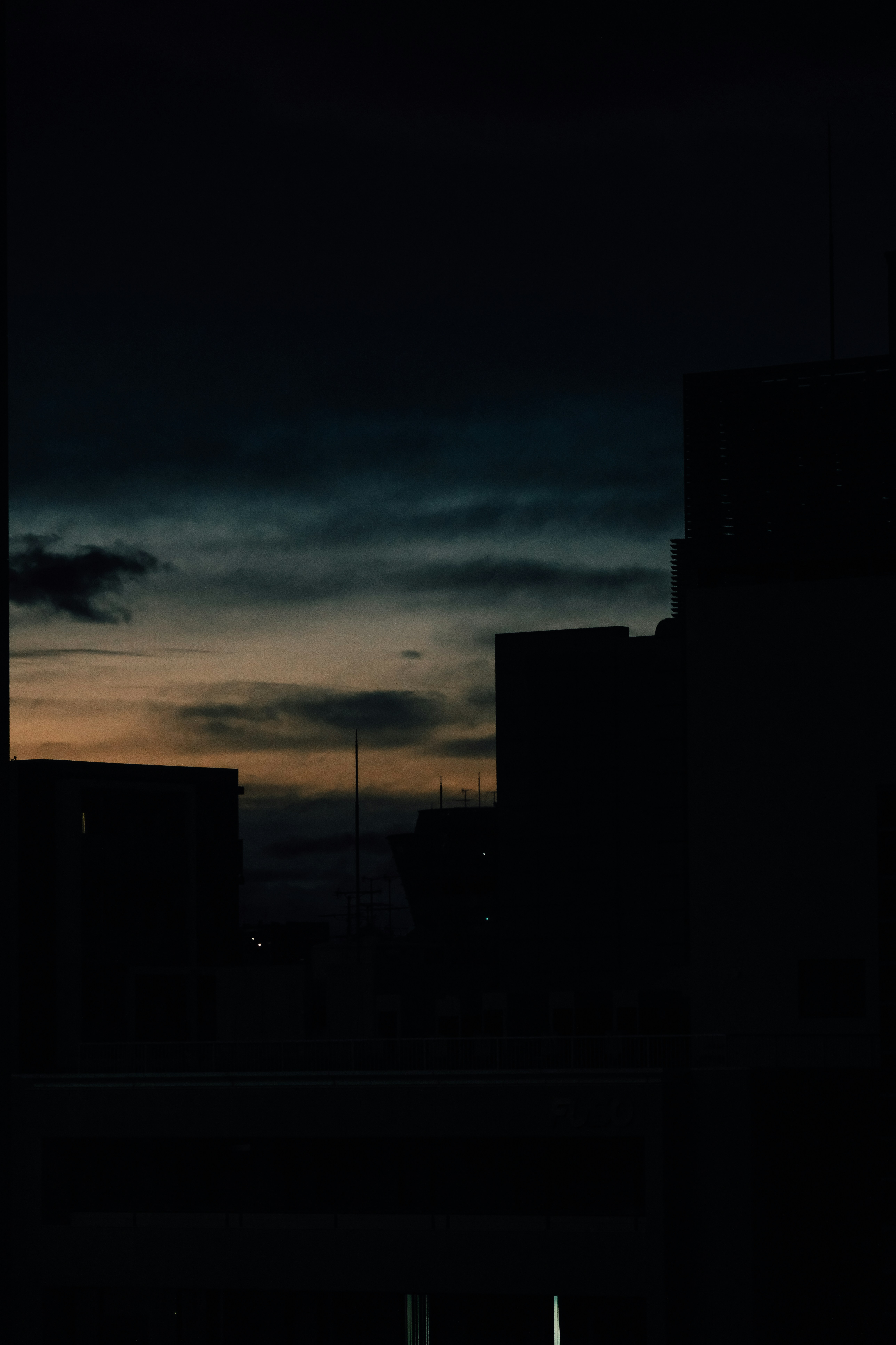 Dark buildings silhouetted against a cloudy sunset sky