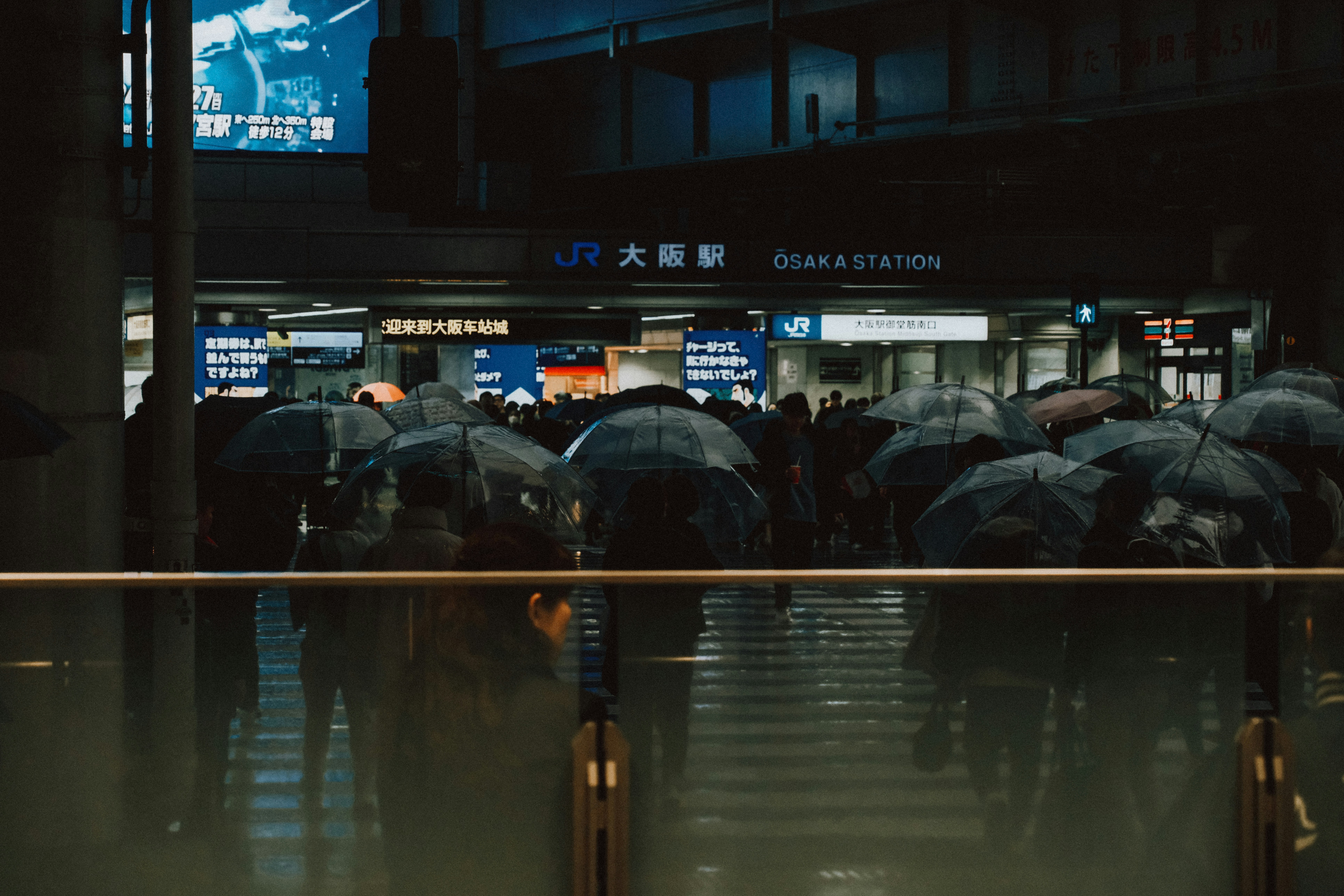 Crowd of commuters under umbrellas at Osaka Station during a rainy evening, showcasing the urban atmosphere.