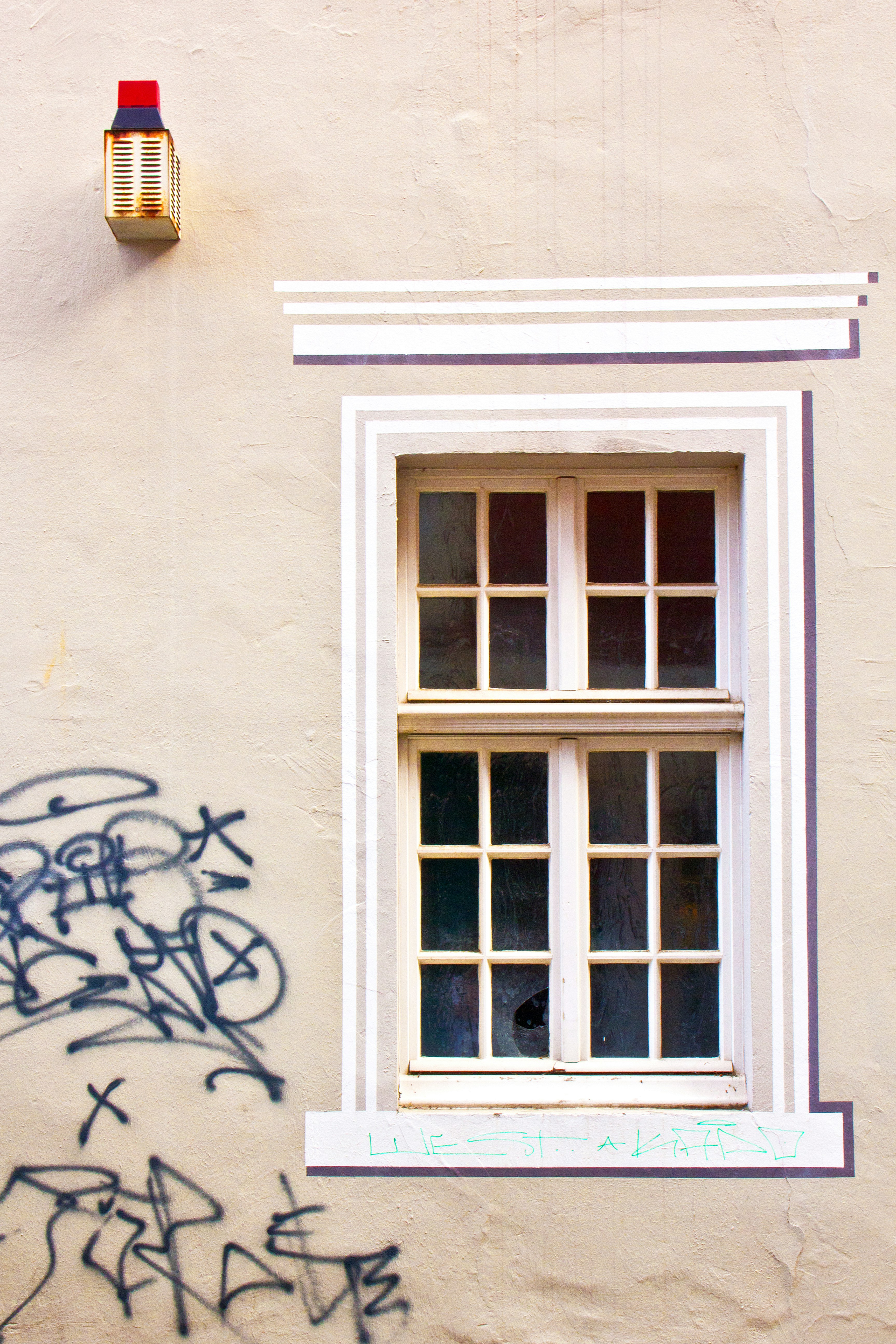 A decorative window framed by minimalist lines, juxtaposed with vibrant graffiti on a textured wall.