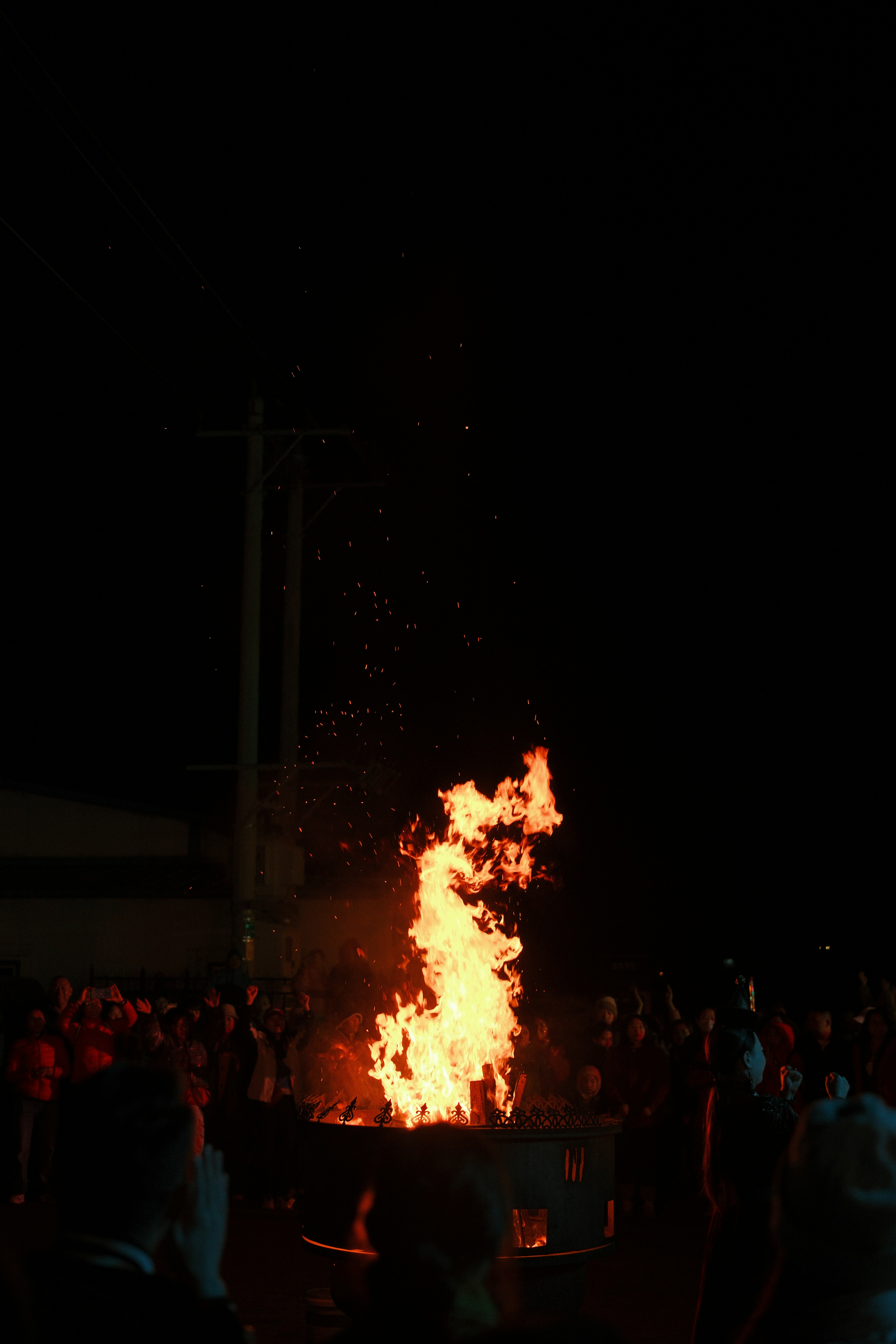A large bonfire burns brightly at night with spectators.