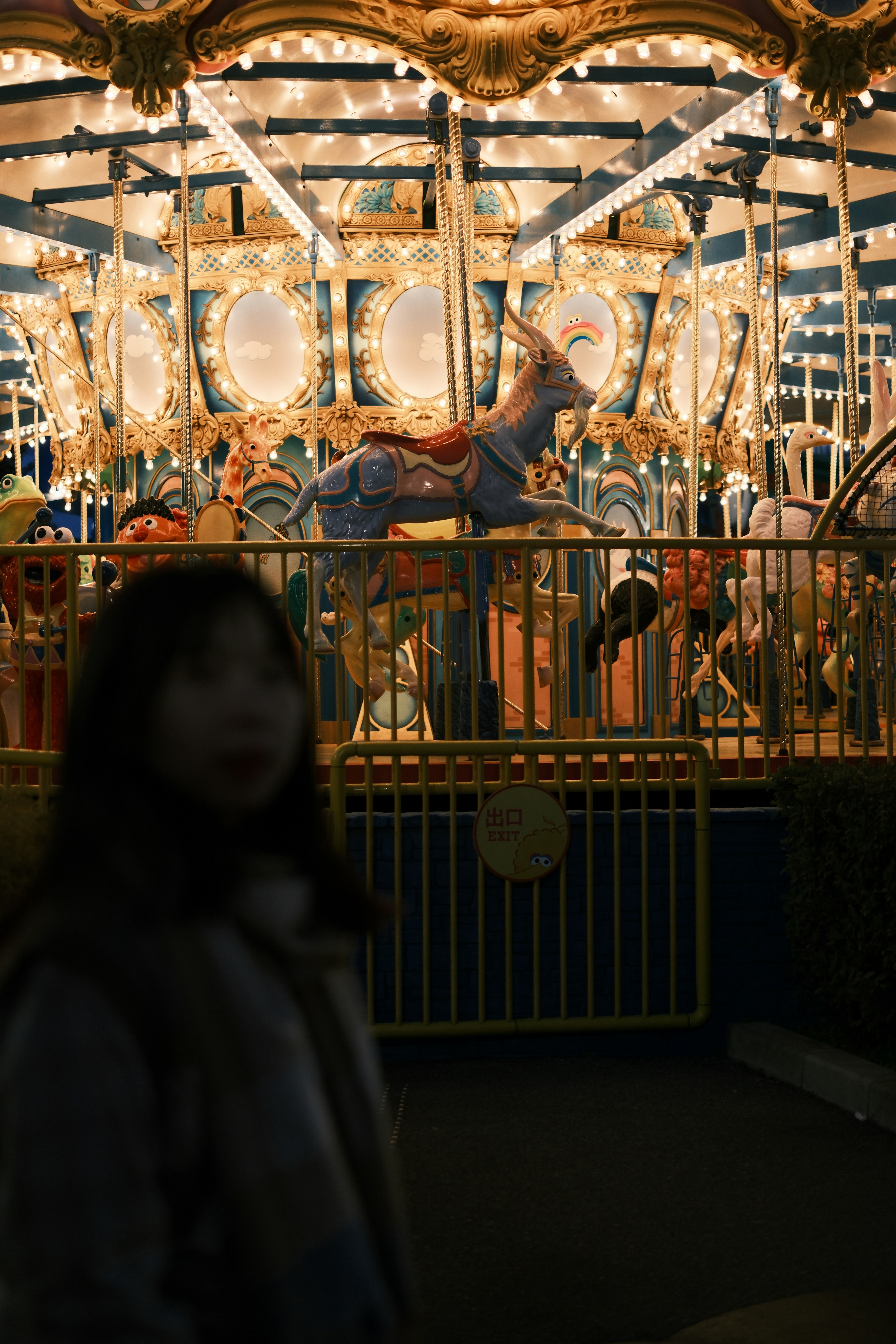 Woman in front of brightly lit carousel at night