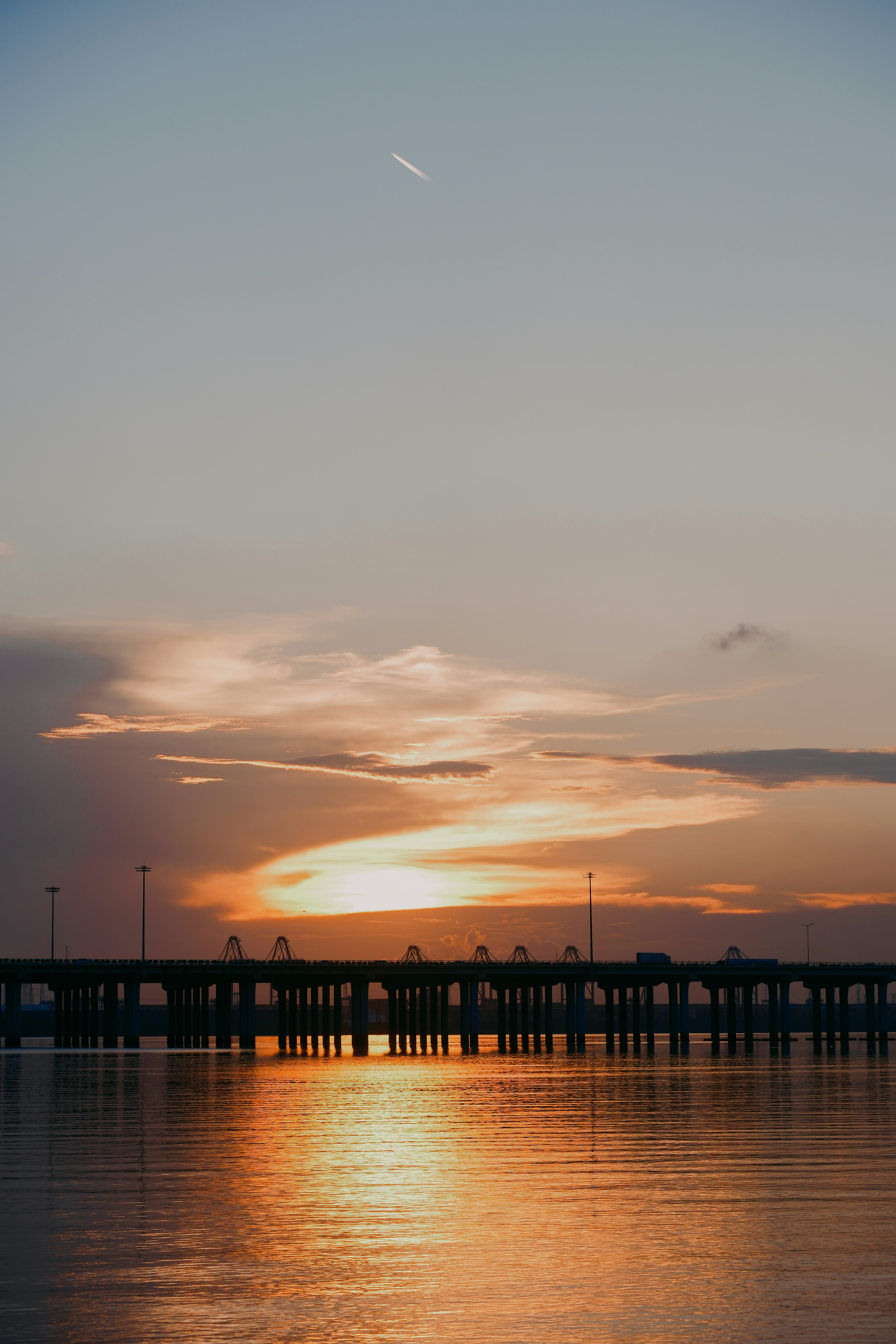 Silhouetted bridge against a vibrant sunset reflecting on calm waters.