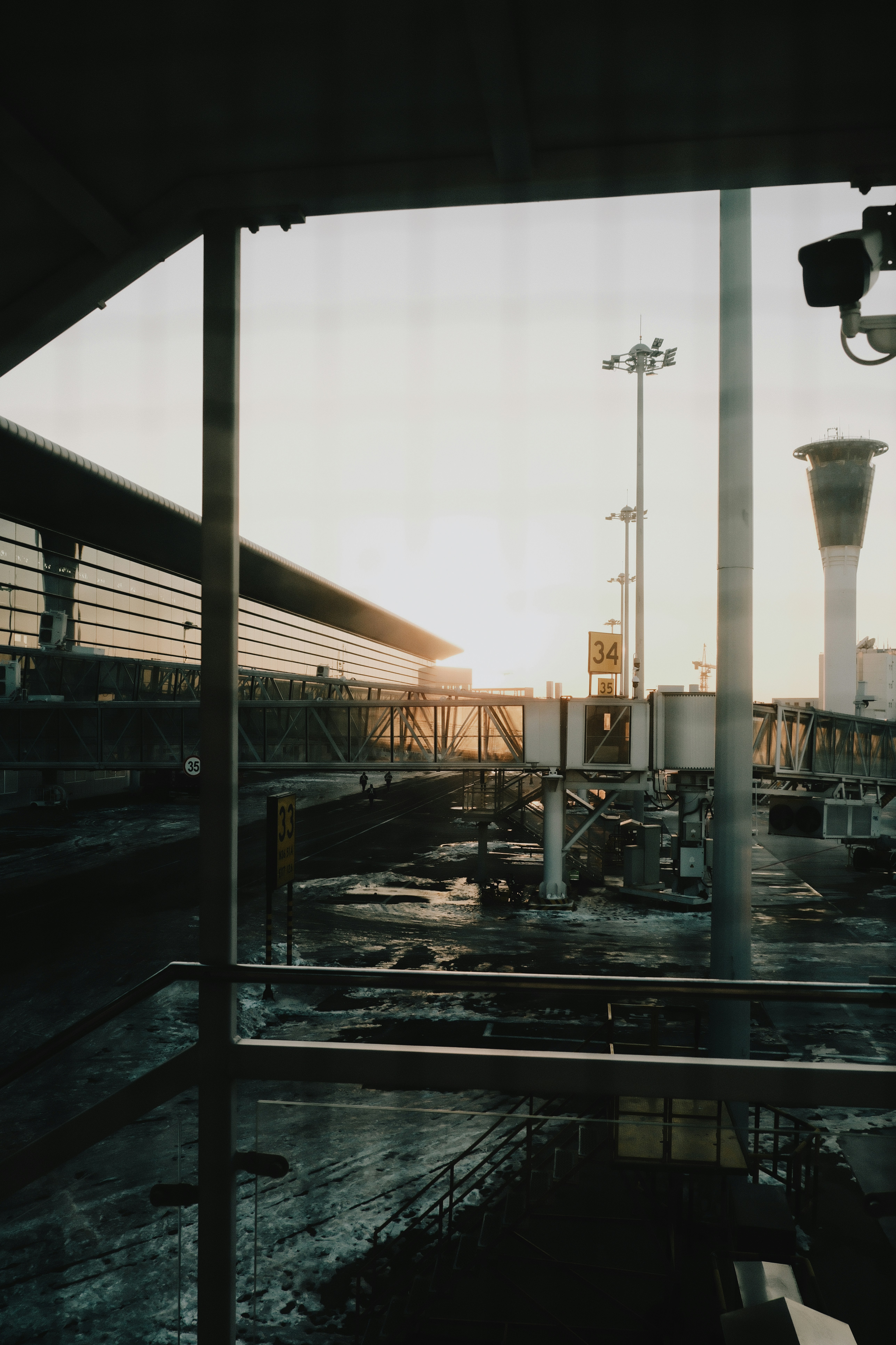 Airport terminal at sunrise, showcasing the runway and jet bridges framed by modern architecture. The soft light adds a serene ambiance.