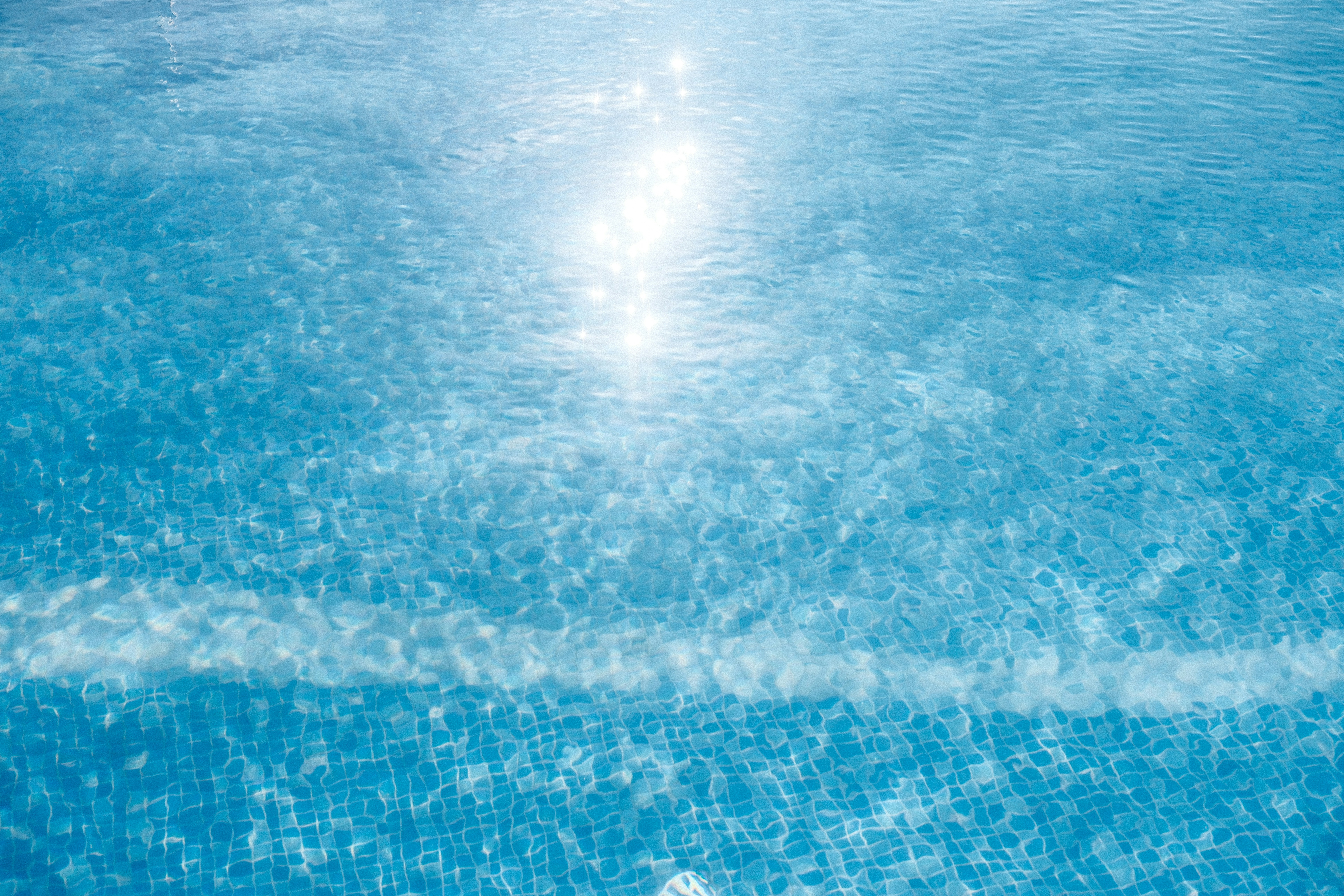 Sunlight reflects on the surface of a blue swimming pool.