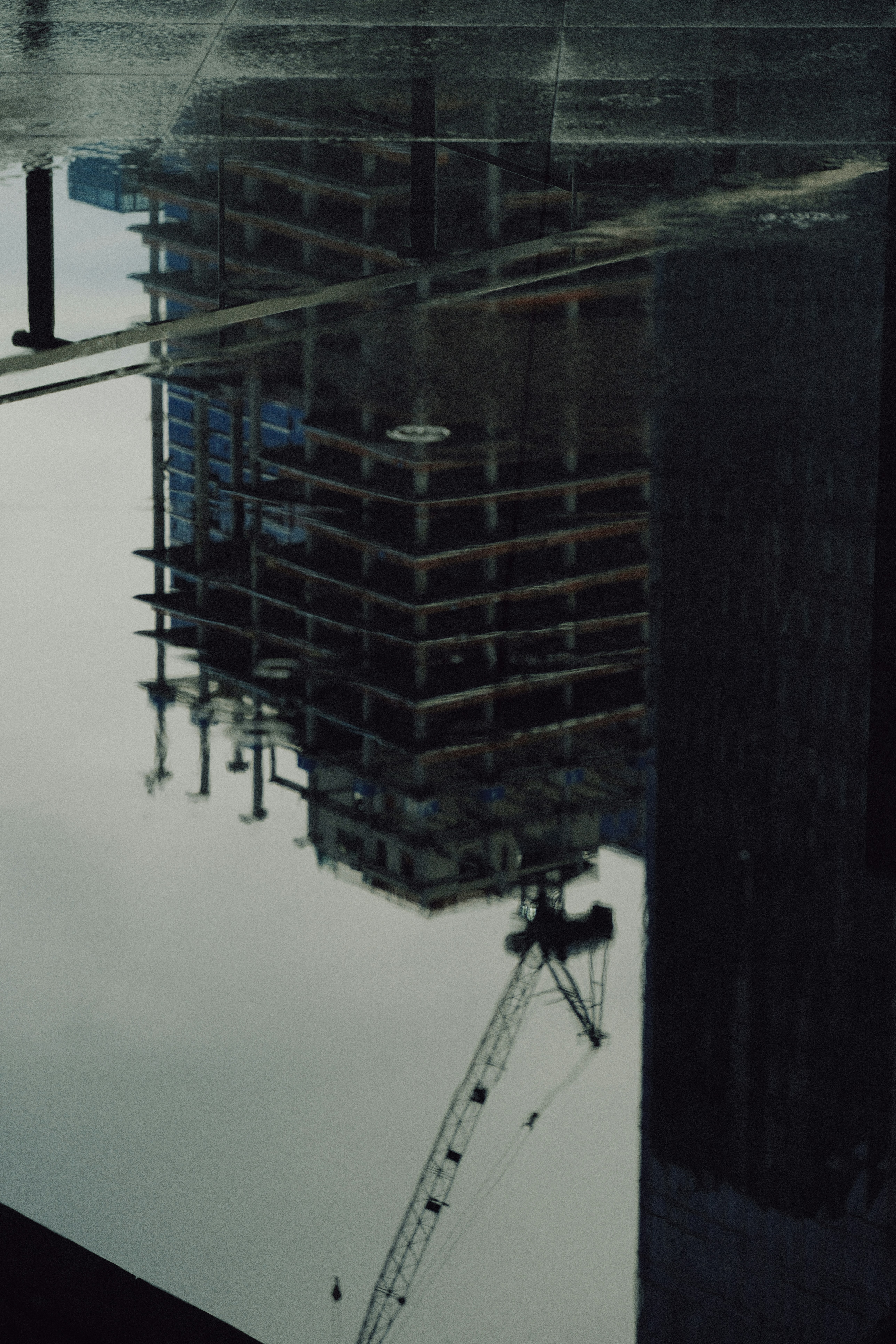 Building reflection in a puddle with a crane.