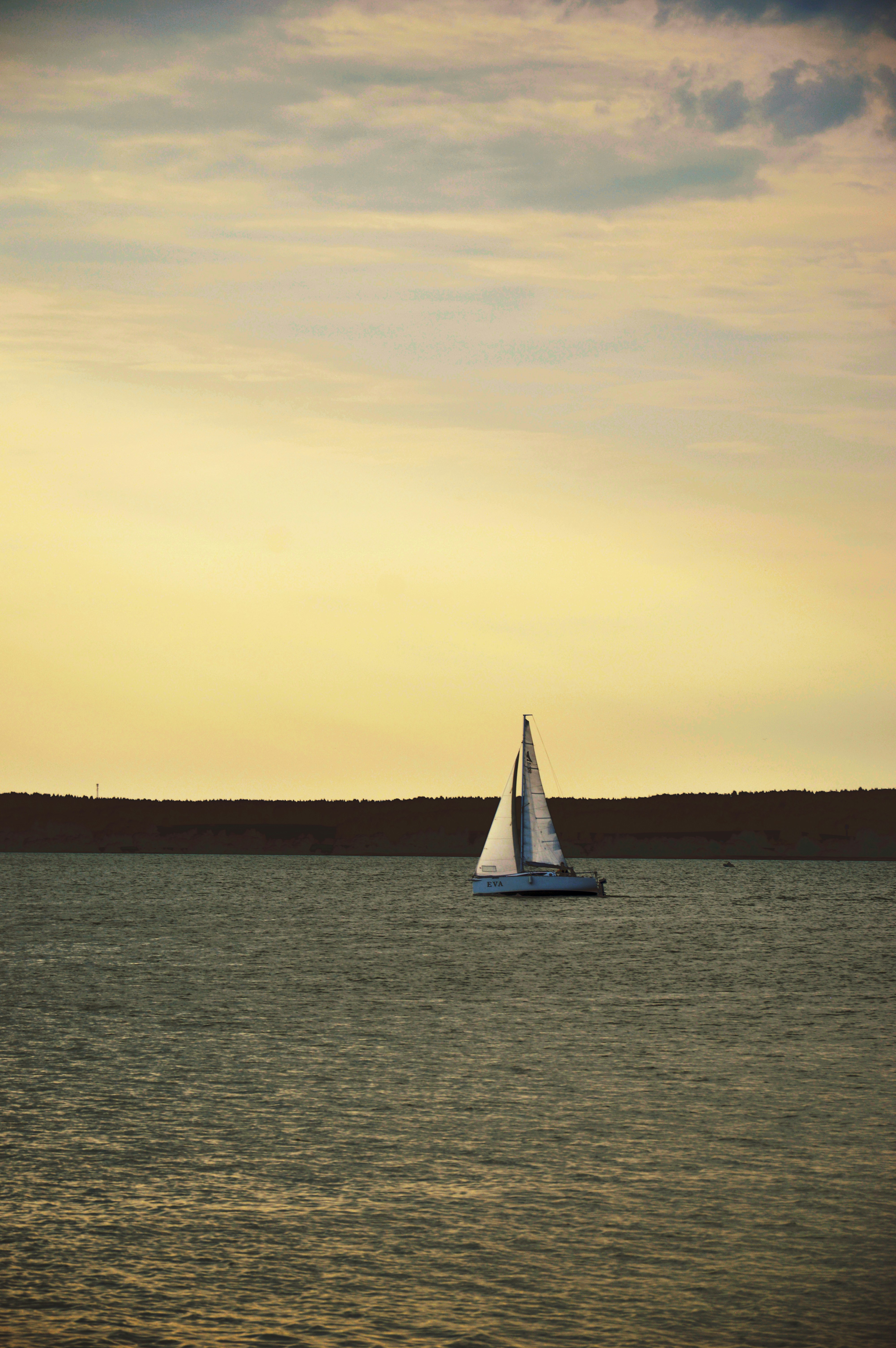 A sailboat glides across the water at sunset.