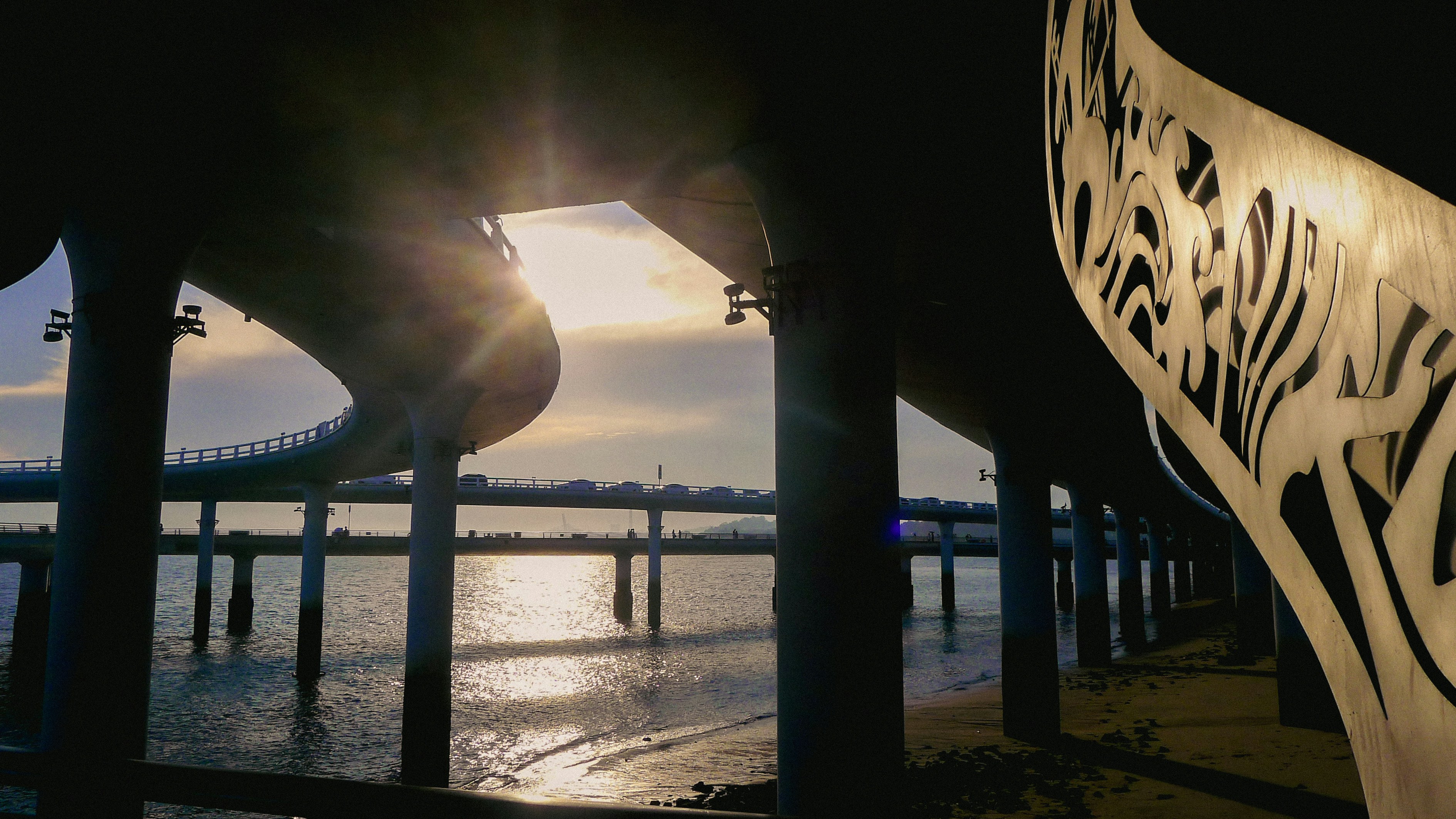 Under a bridge with water and sky at sunset