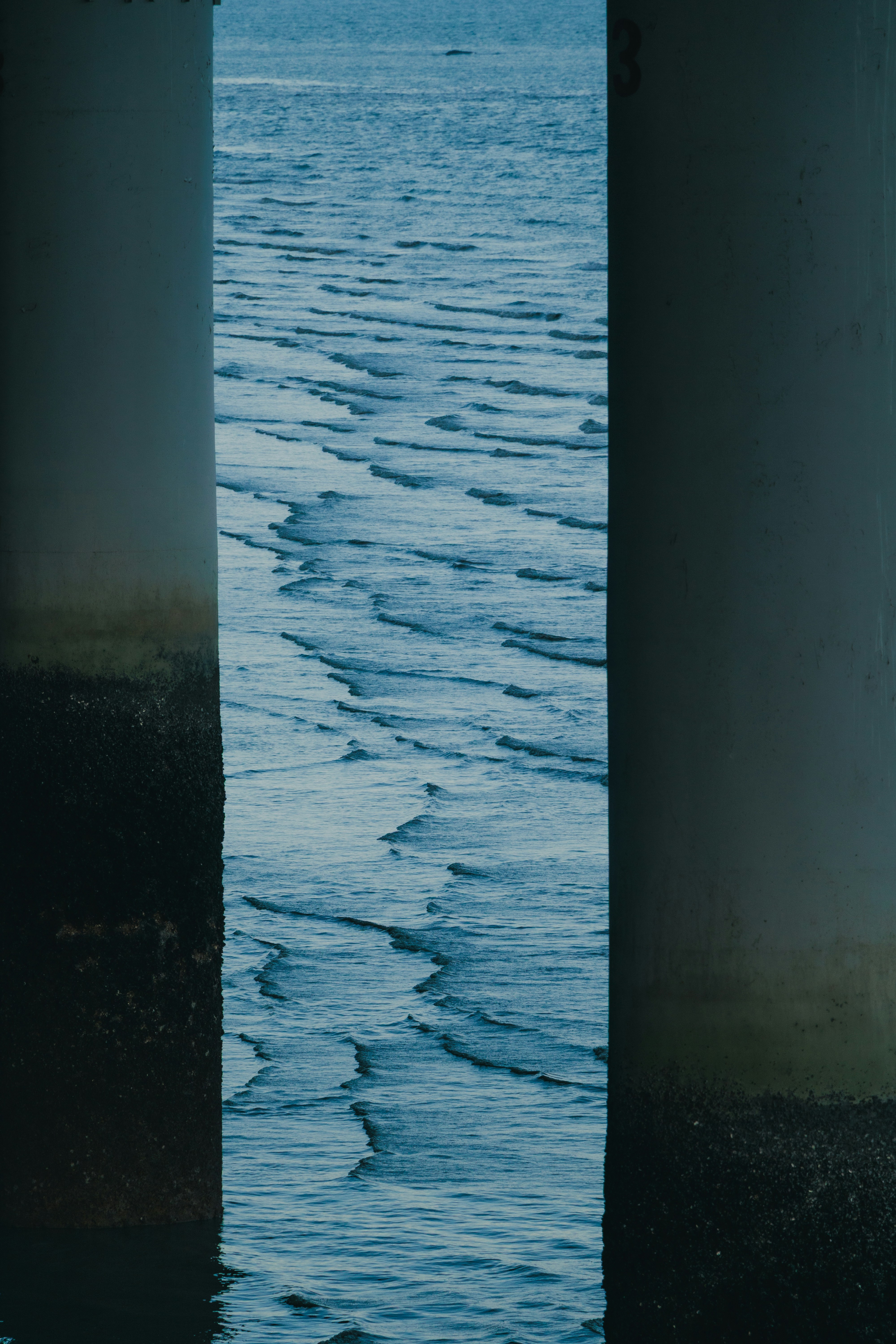 Rippled blue water seen between two concrete pillars.