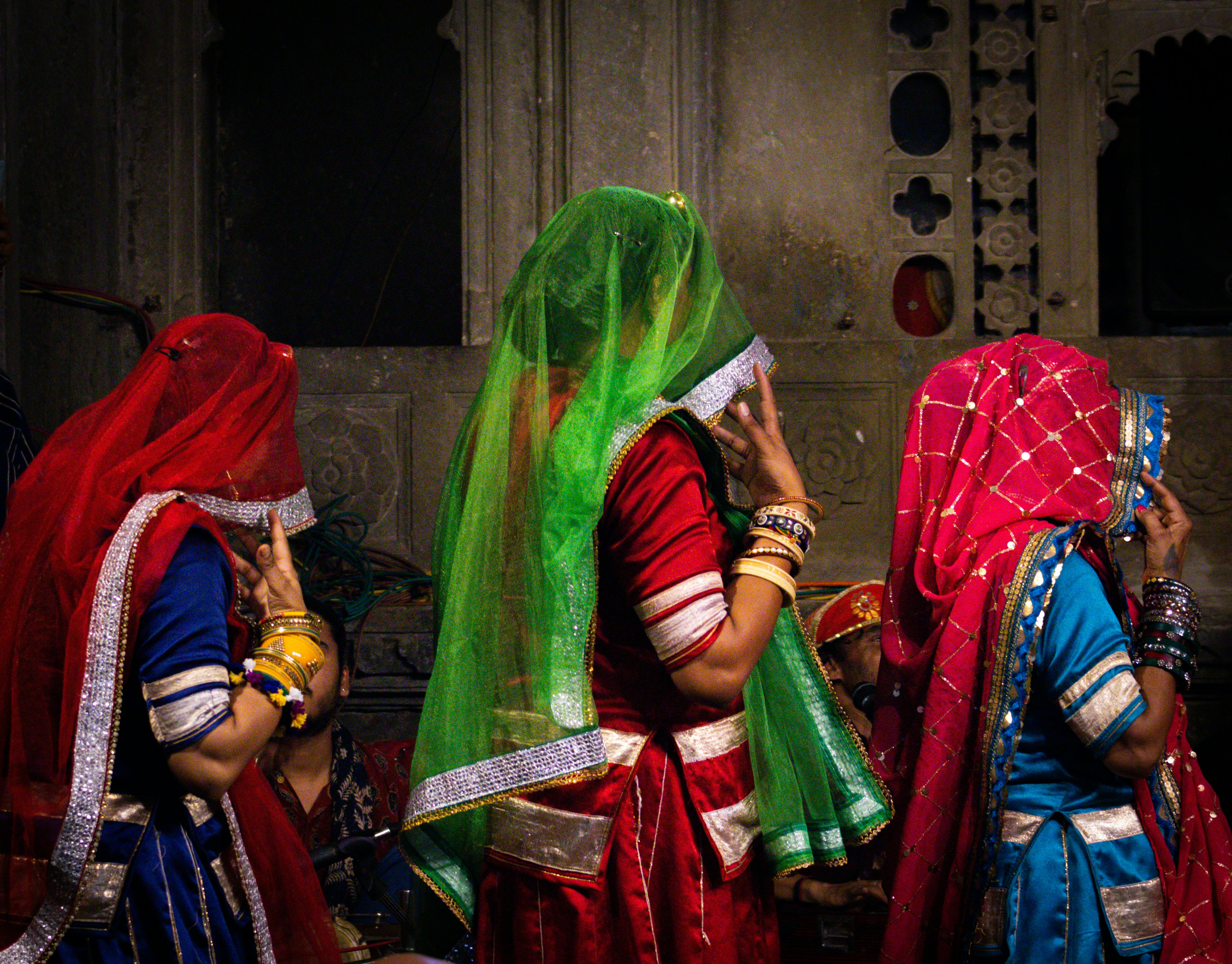 Three women adorned in vibrant traditional attire and veils engage in a cultural ritual, embodying the spirit of celebration.