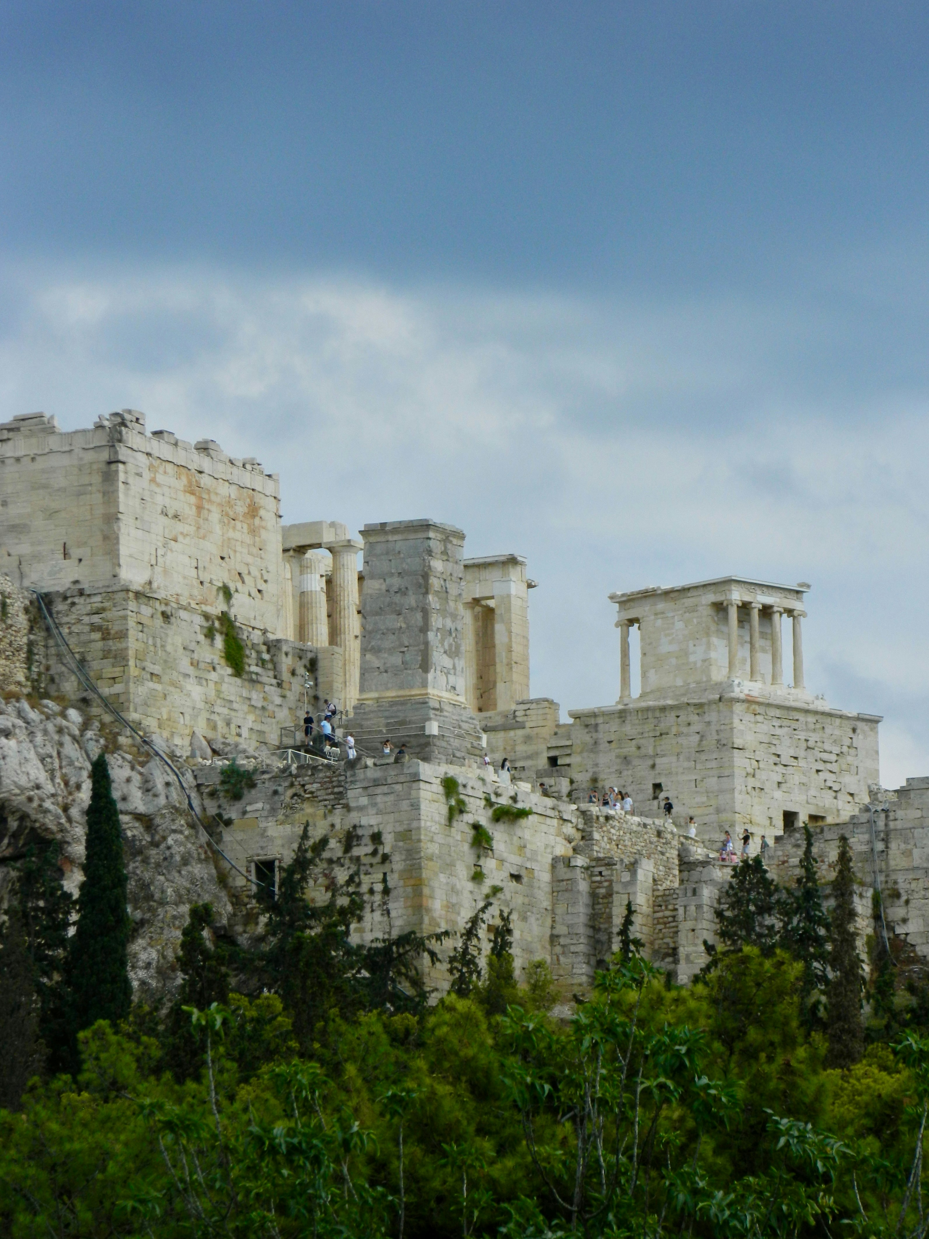 Athens #43 | Ancient stone structures on a hill under cloudy sky.