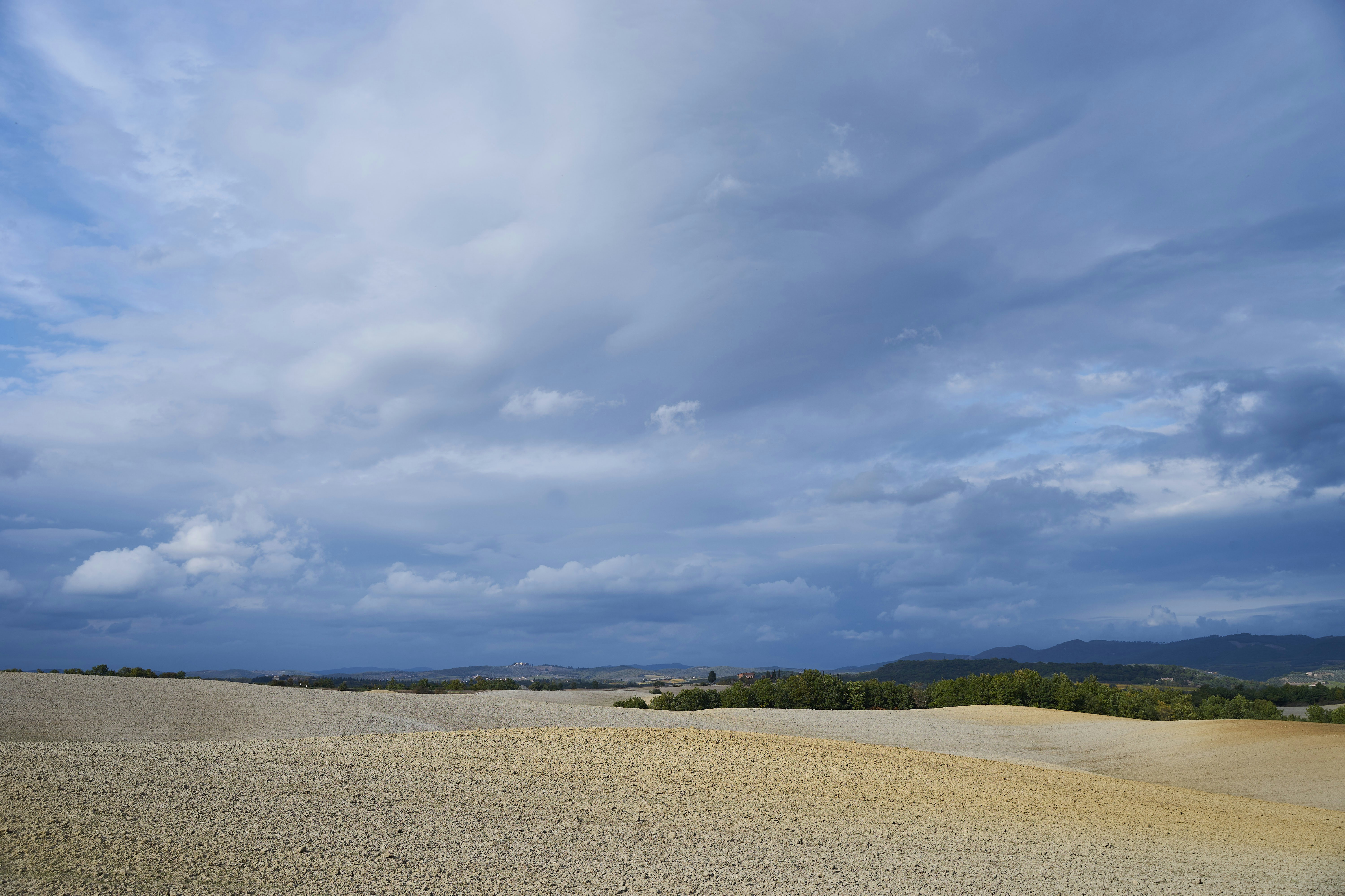 Expansive landscape featuring gently rolling hills under a dramatic sky, showcasing the interplay of light and shadow across the terrain.