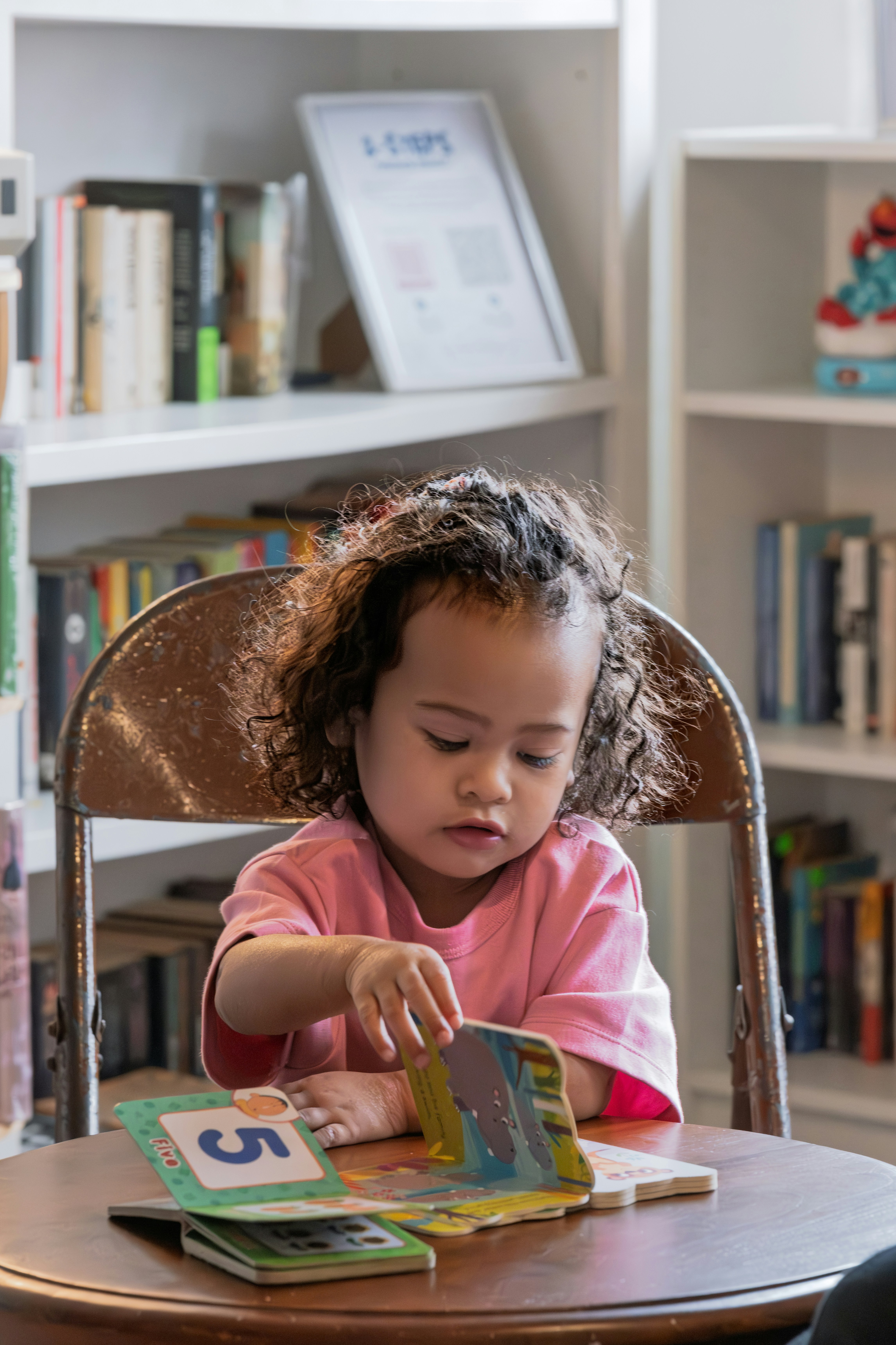 Young child engrossed in a colorful counting book, seated at a wooden table in a cozy library setting.