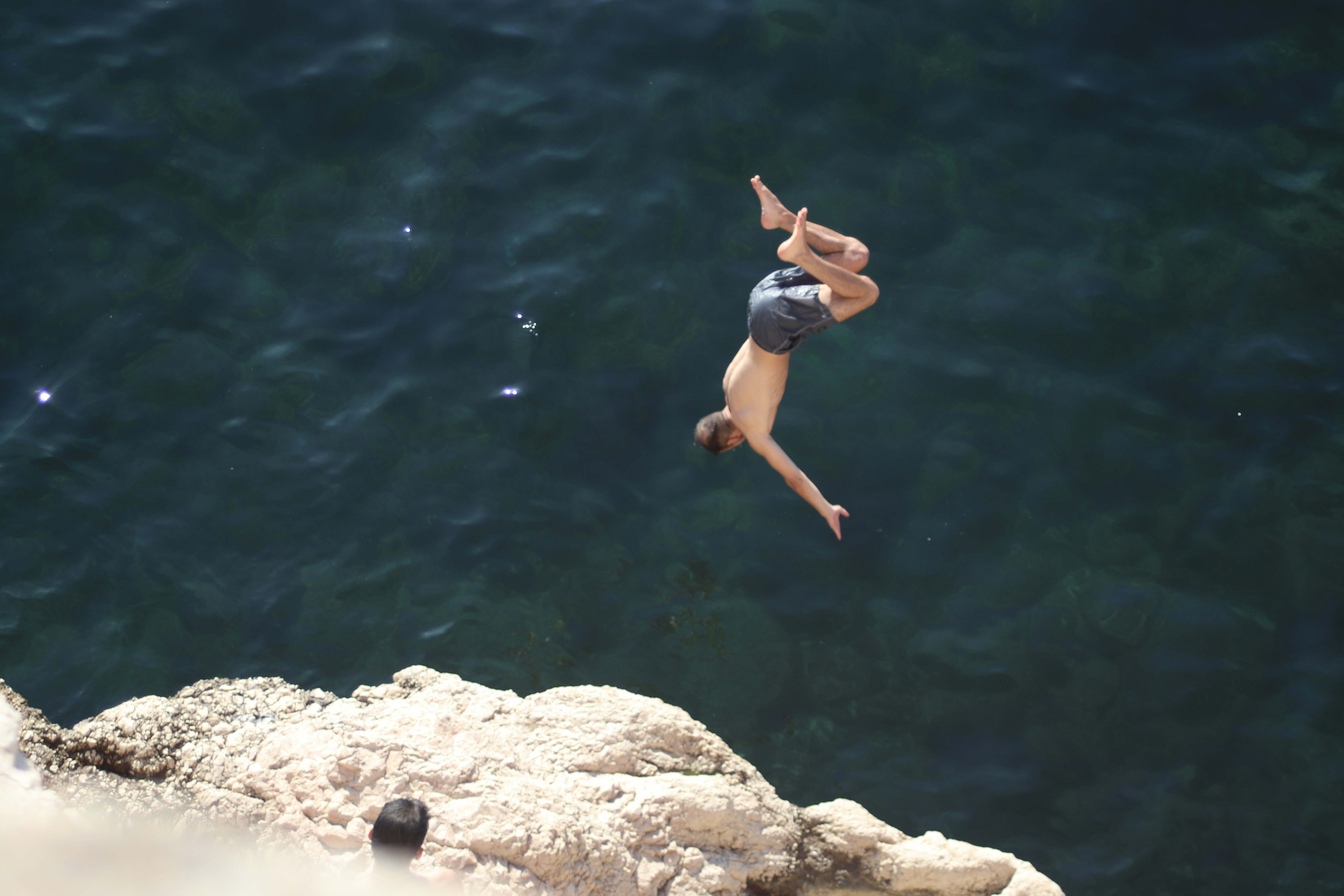 Man performs a backflip while cliff diving into water