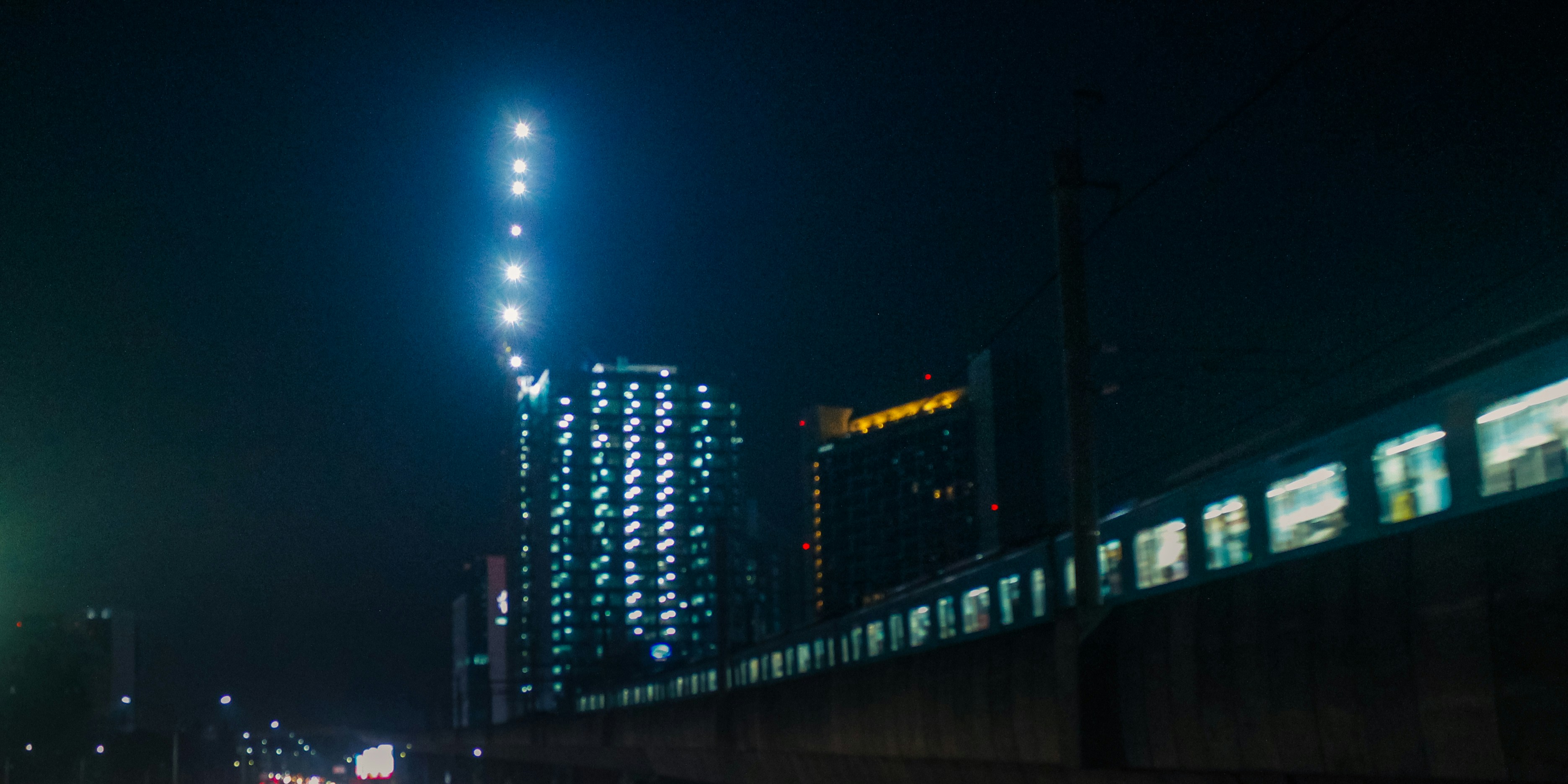 Cityscape Jakarta | Train moving past illuminated city buildings at night