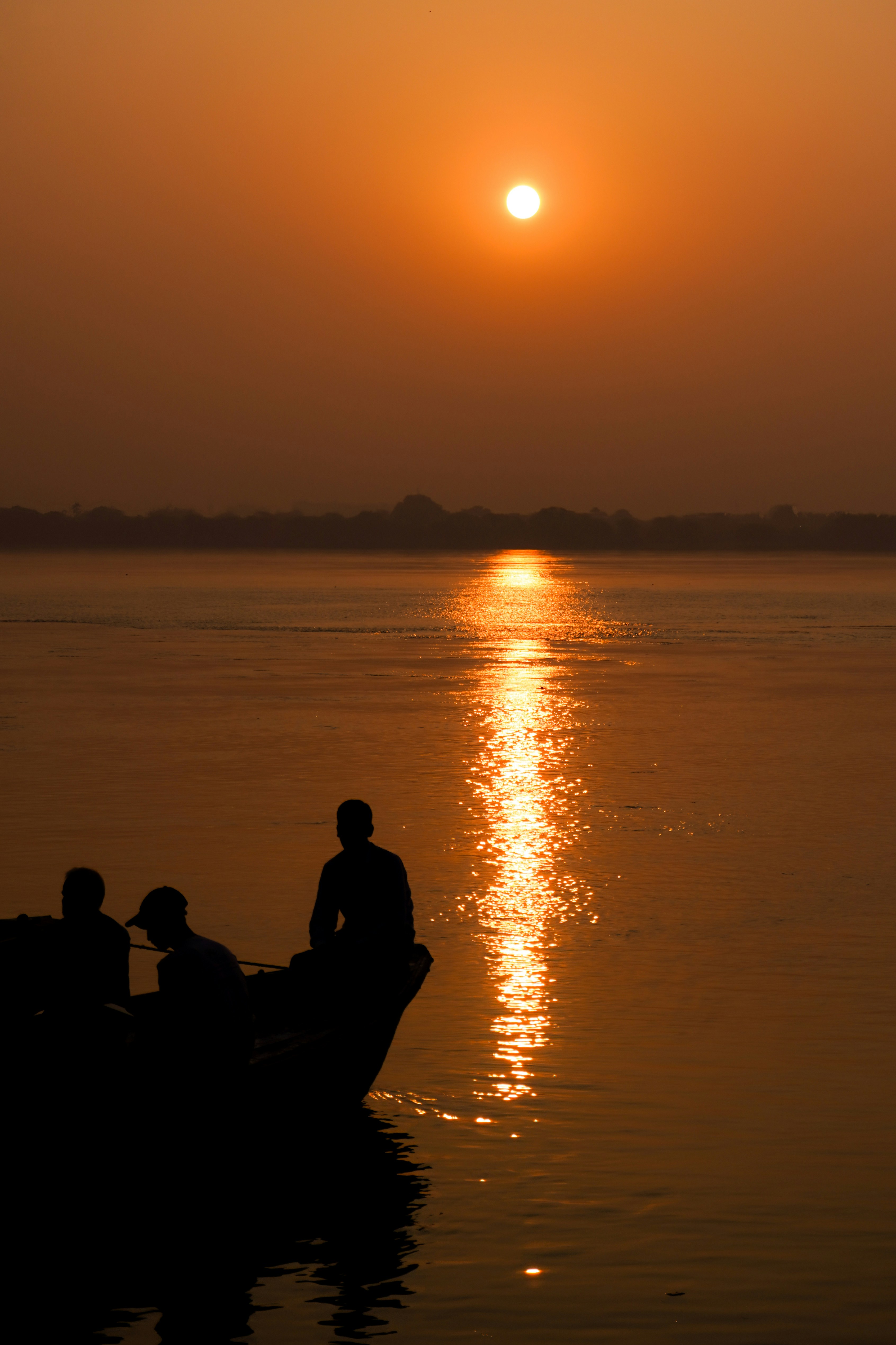 Sunrise at Assi Ghat in Varanasi | Silhouetted people in a boat at sunset on a river.
