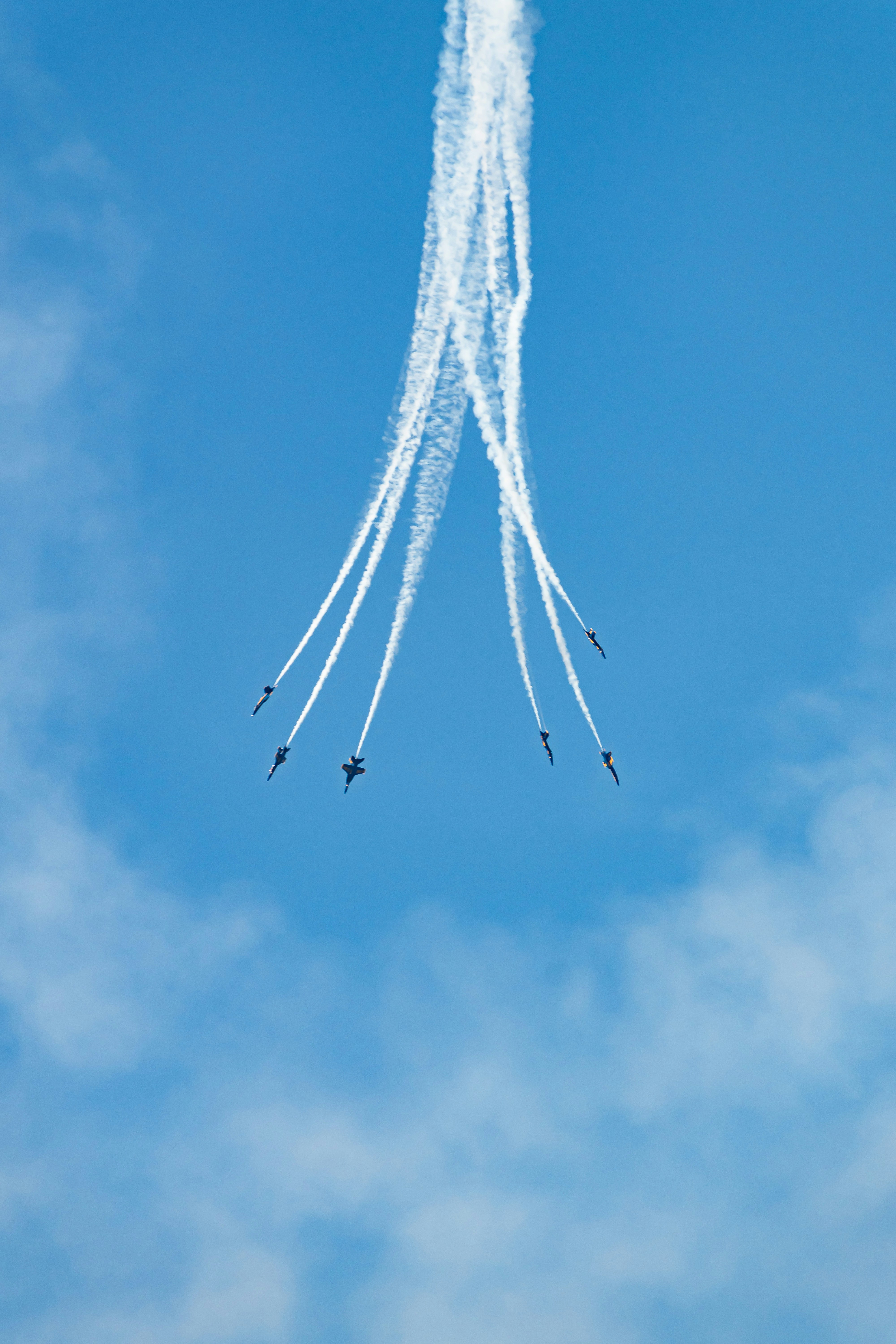 Five fighter jets performing a synchronized maneuver, leaving trails of smoke against a clear blue sky.