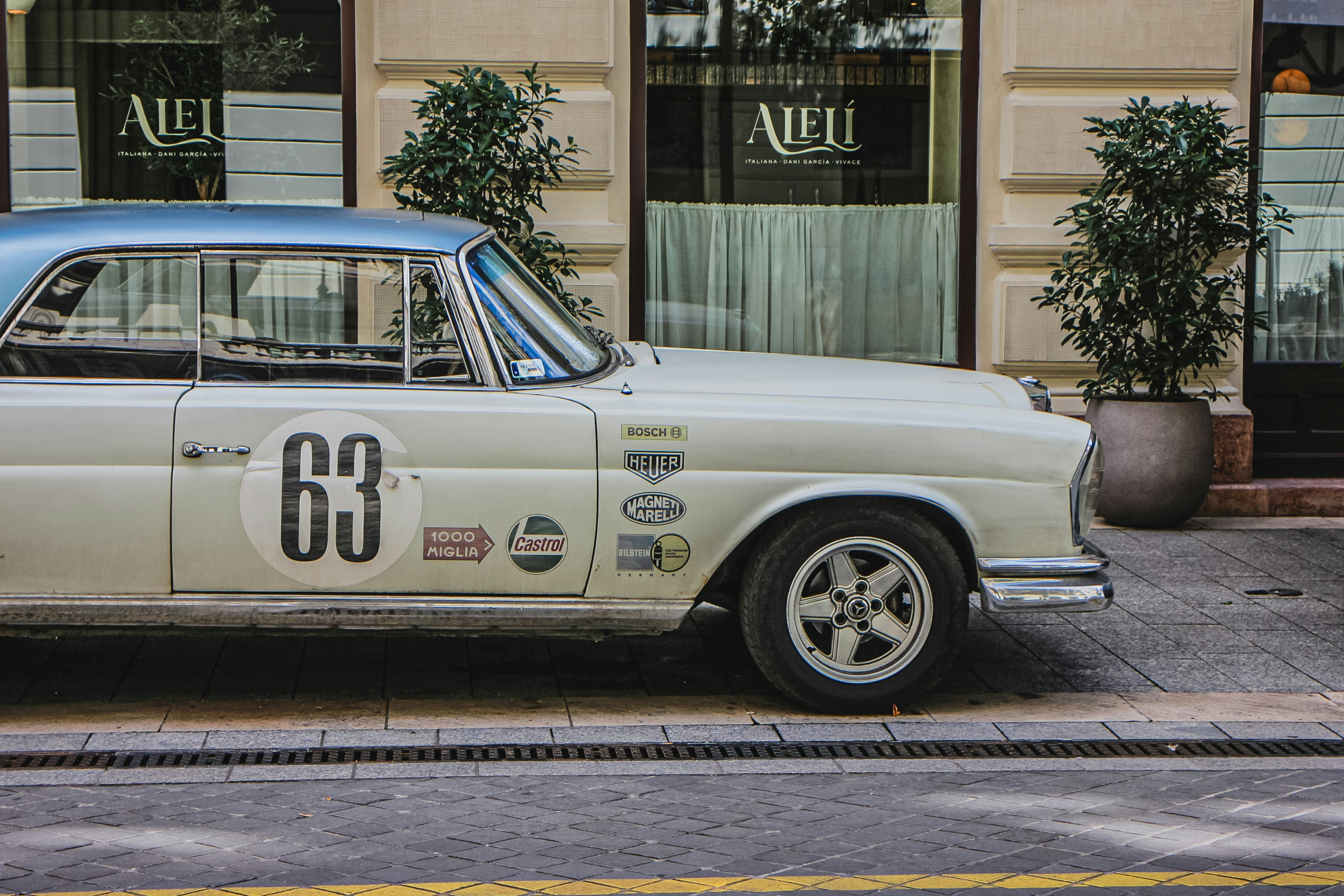 Classic vintage car parked beside a modern café, showcasing its retro charm with racing number 63 displayed prominently.