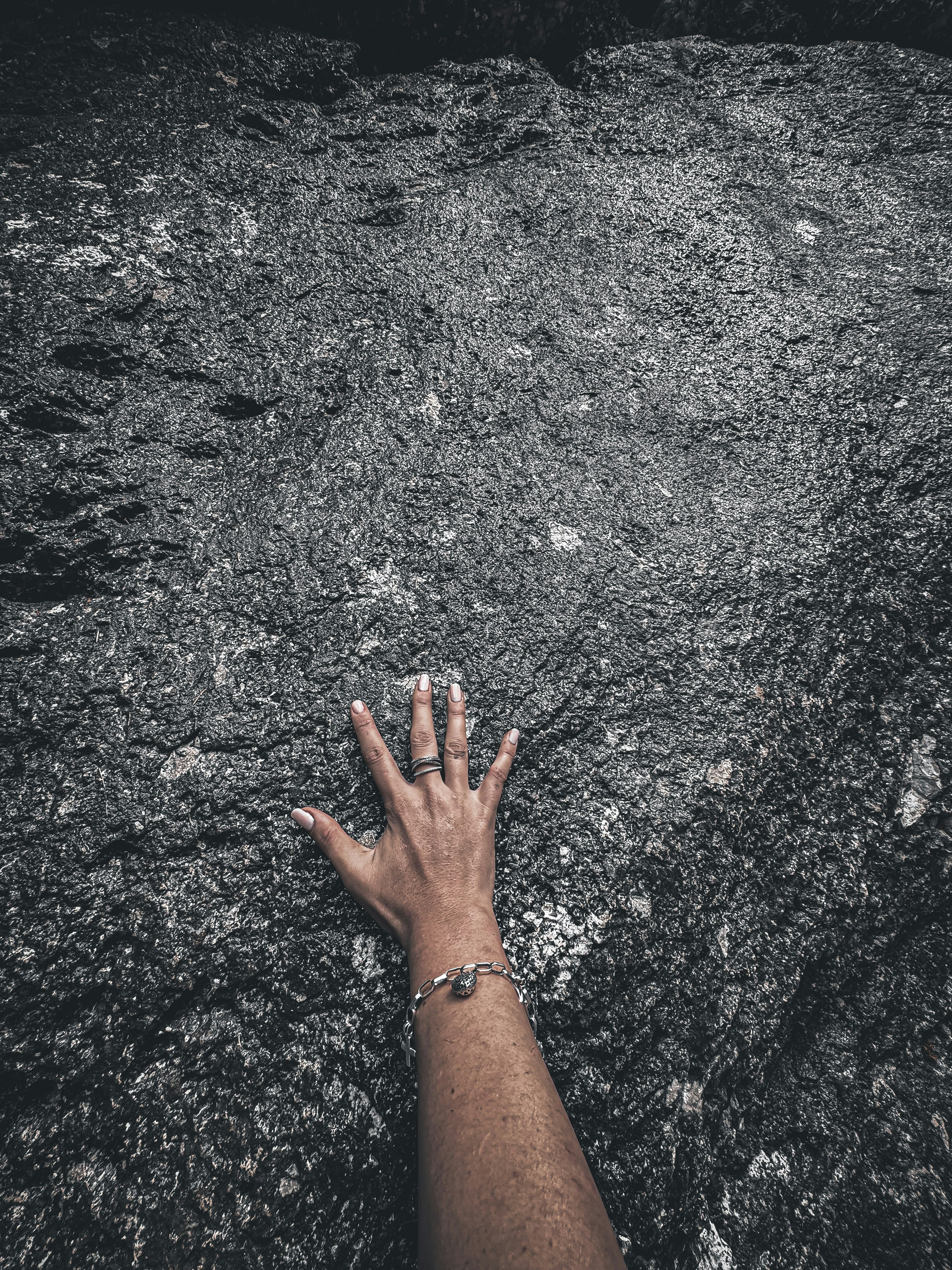 Hand reaching out to feel the rugged surface of a rock, highlighting the contrast between human touch and natural elements.