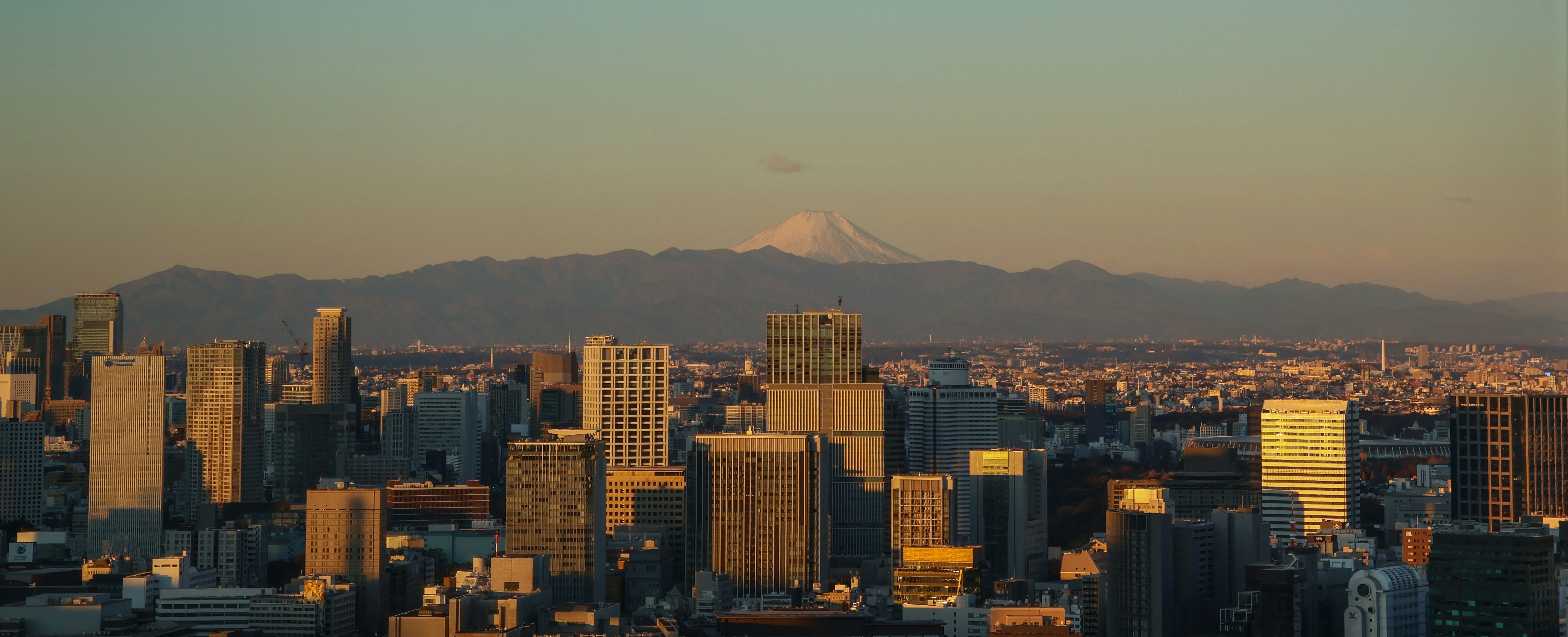 Tokyo's skyline illuminated by the golden hour, with Mount Fuji subtly rising in the background.
