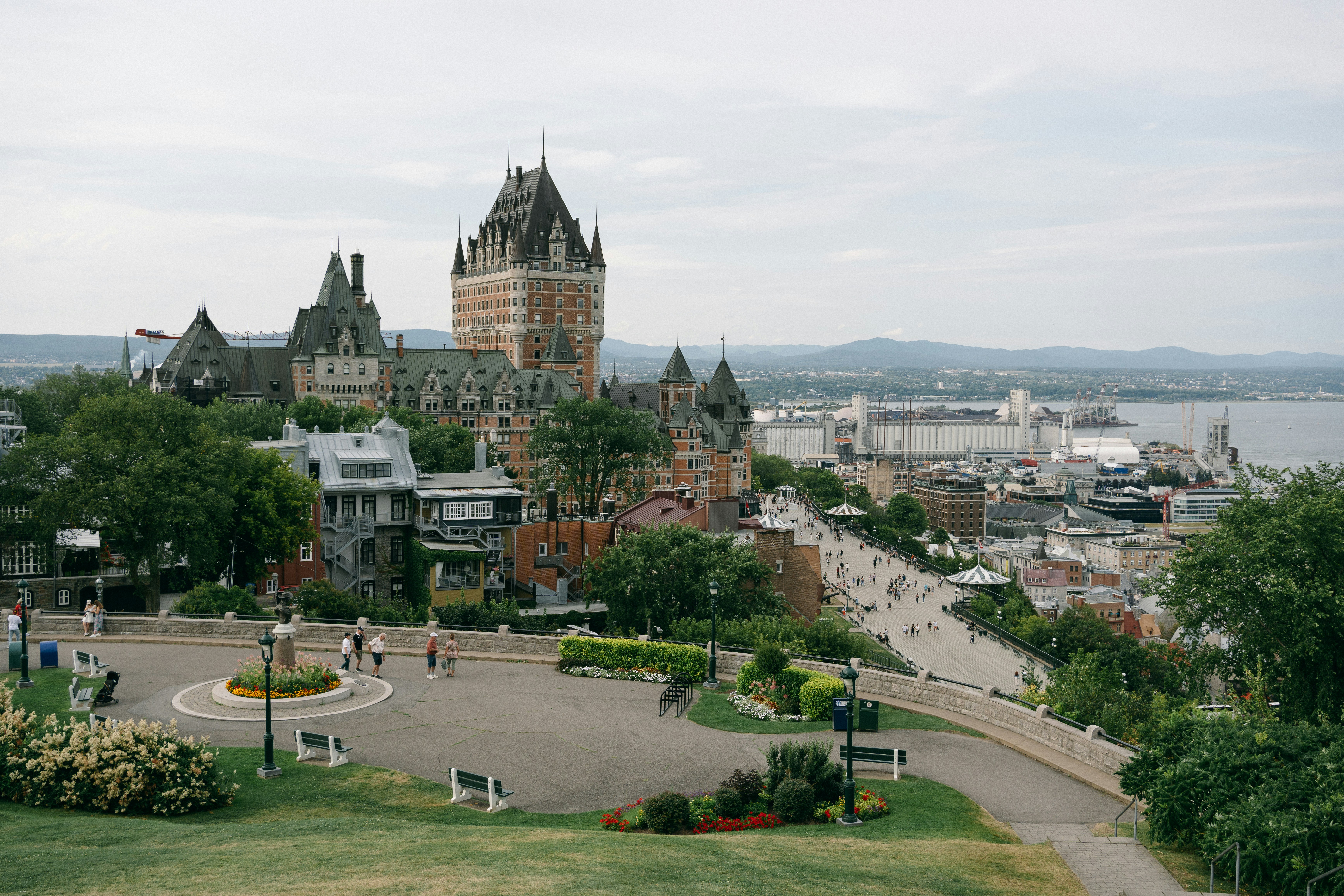 A panoramic view of Quebec City featuring the iconic Château Frontenac, lush greenery, and bustling waterfront activity.