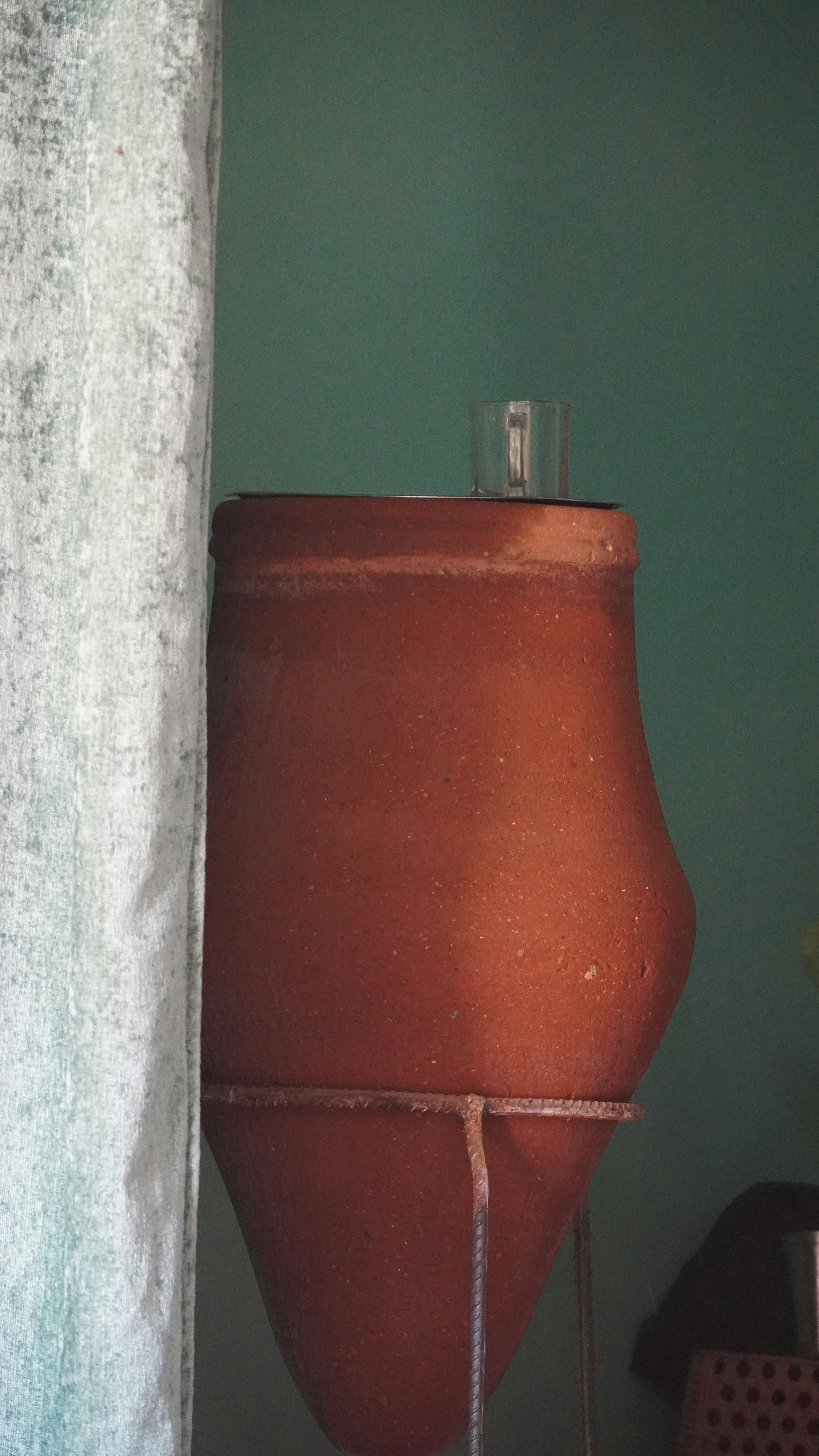 A terracotta amphora with a glass on top.