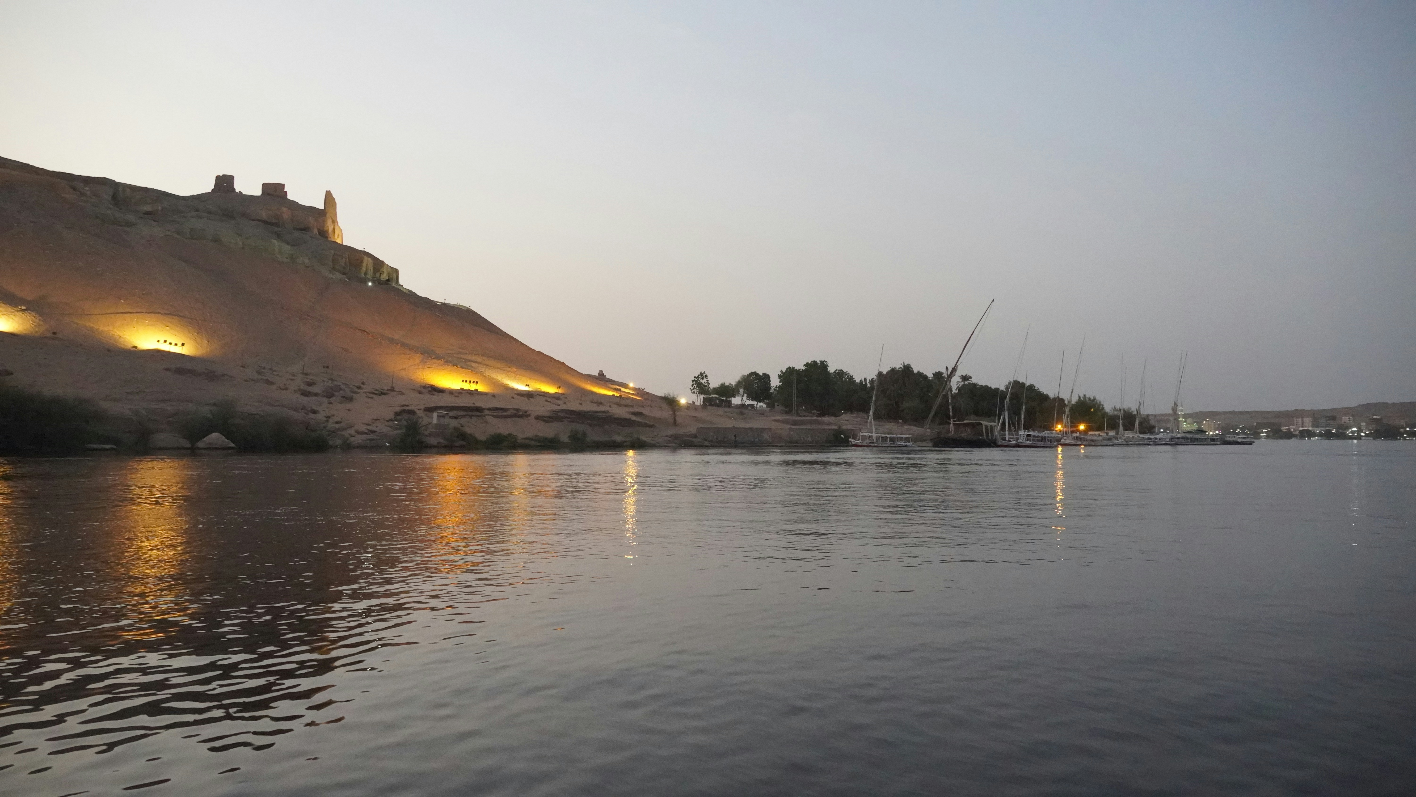 River landscape with illuminated hills and boats at dusk