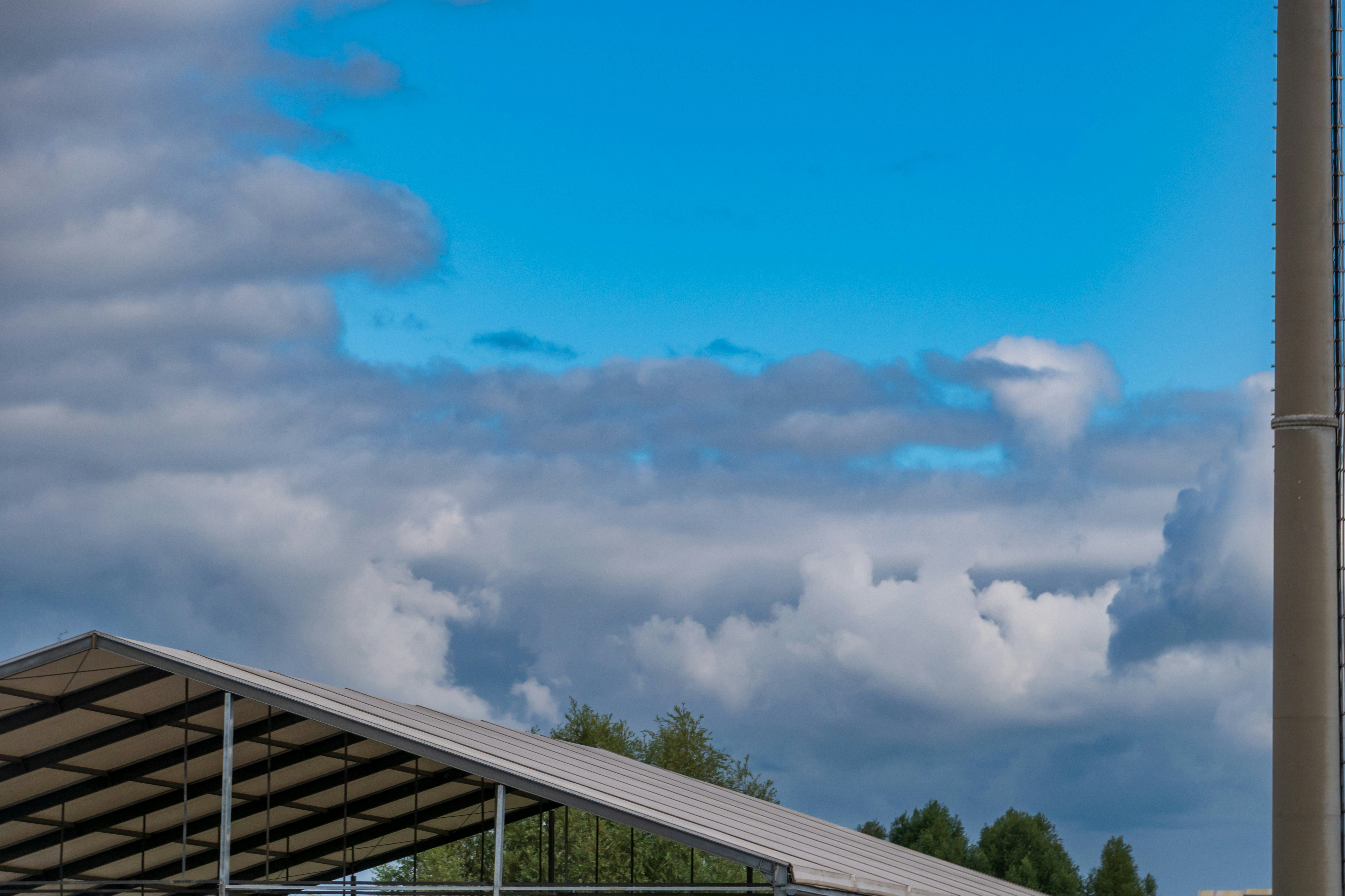 A metal-roofed structure beneath a vast sky filled with dynamic clouds, showcasing the interplay of light and shadow. The scene captures a tranquil moment in nature.