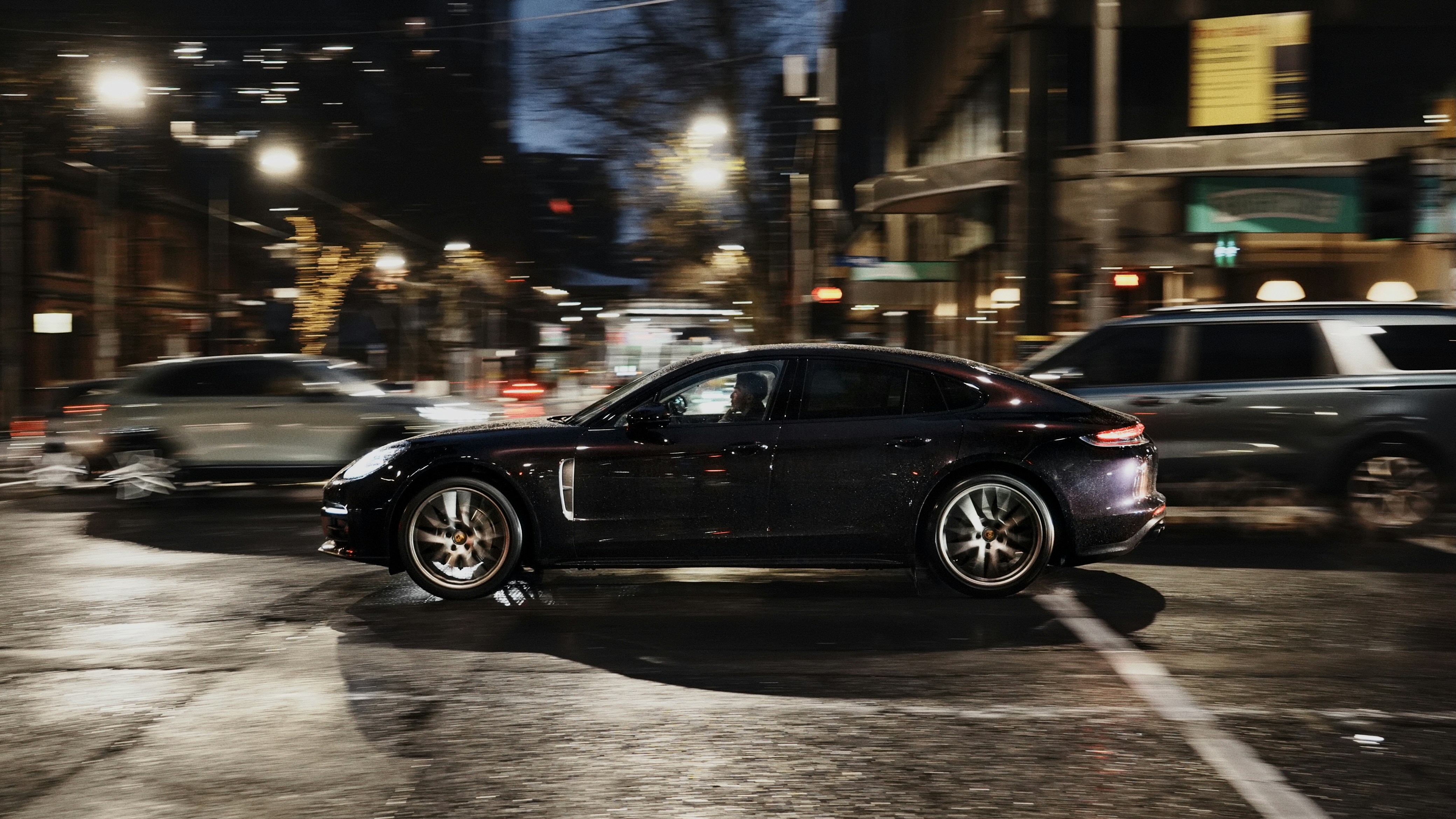 A sleek black car navigating through a bustling city street at night, illuminated by vibrant lights and dynamic motion blur.