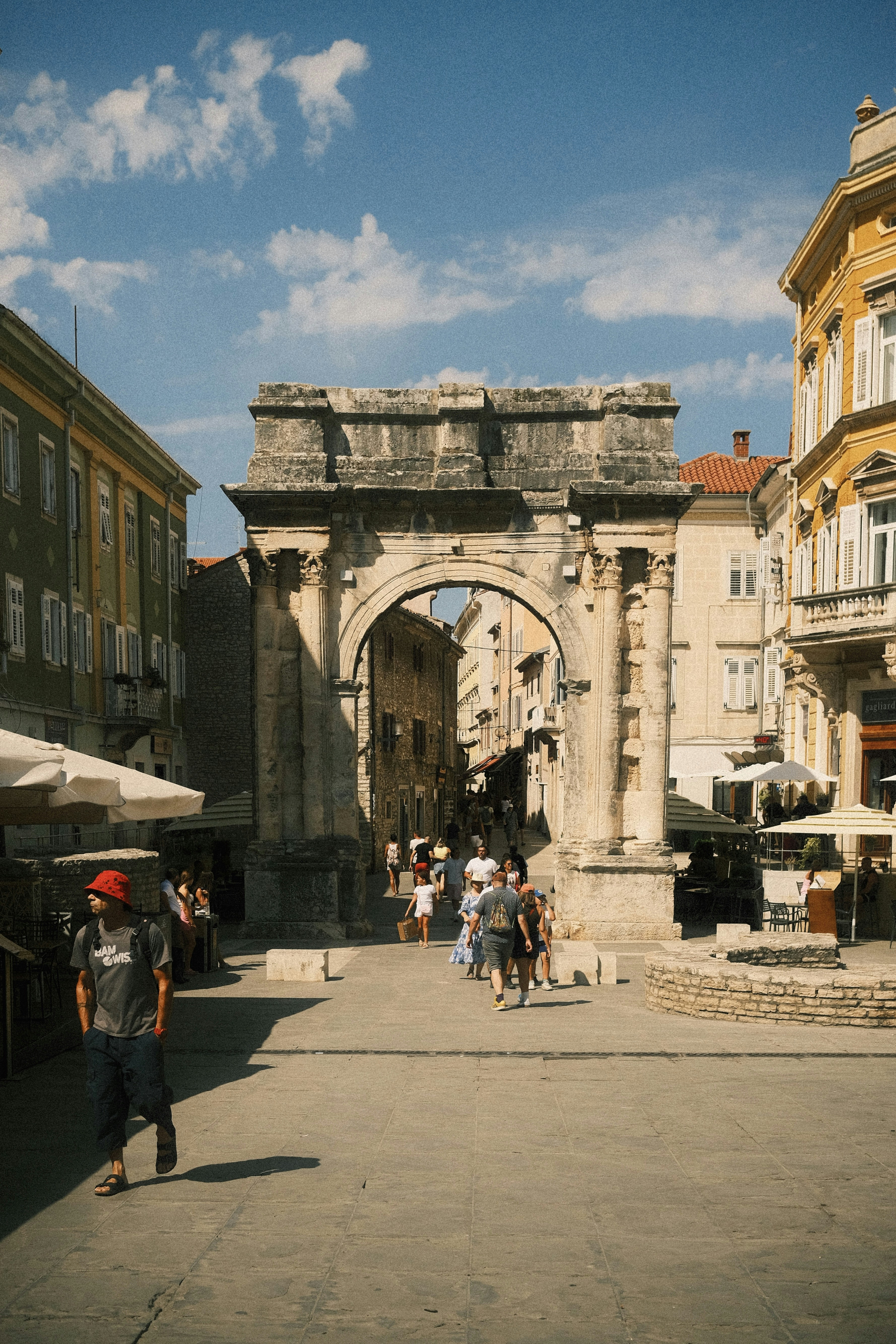 People walk through an ancient stone archway in a plaza. photo – Free ...