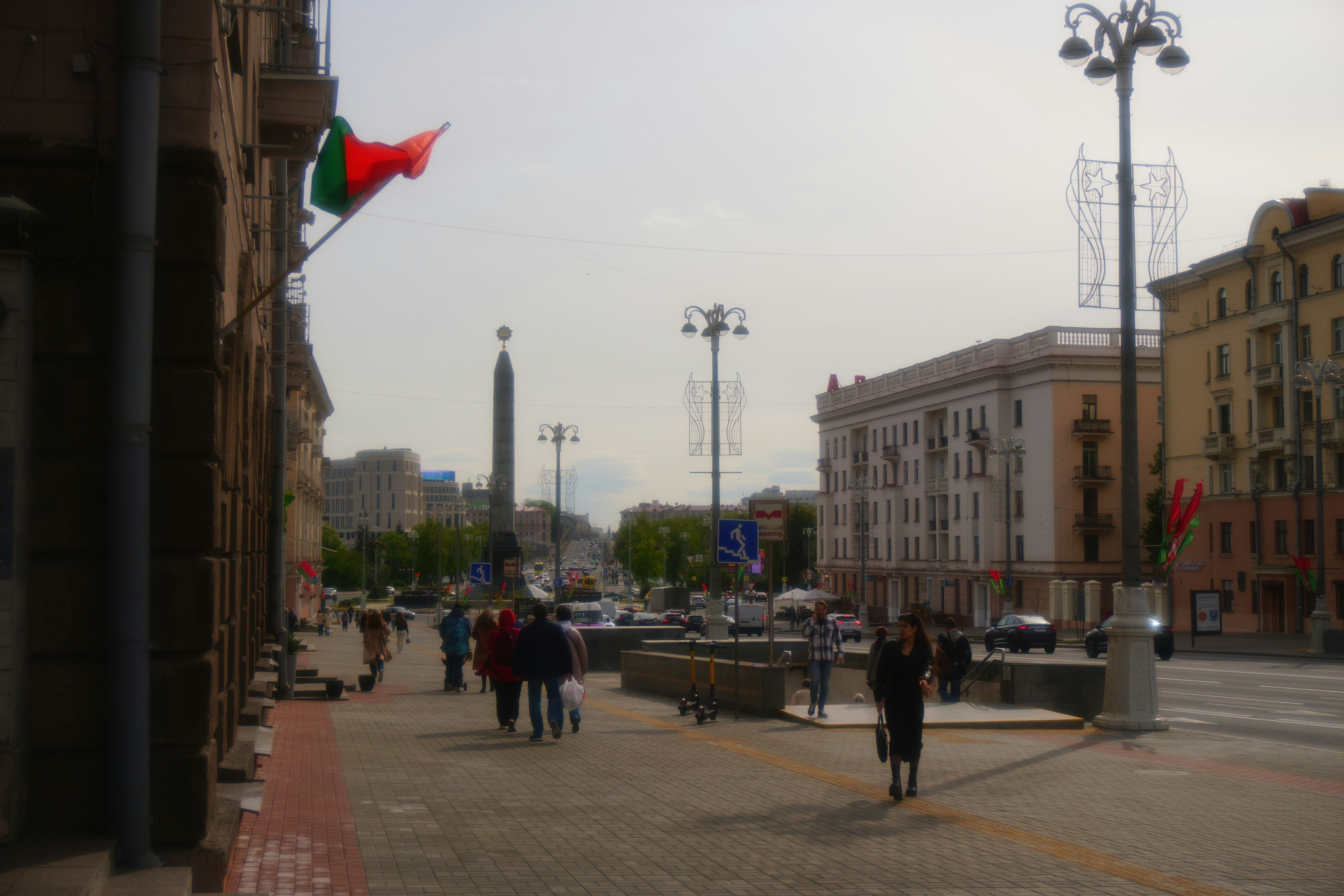 People walking on a city street with buildings and flags.